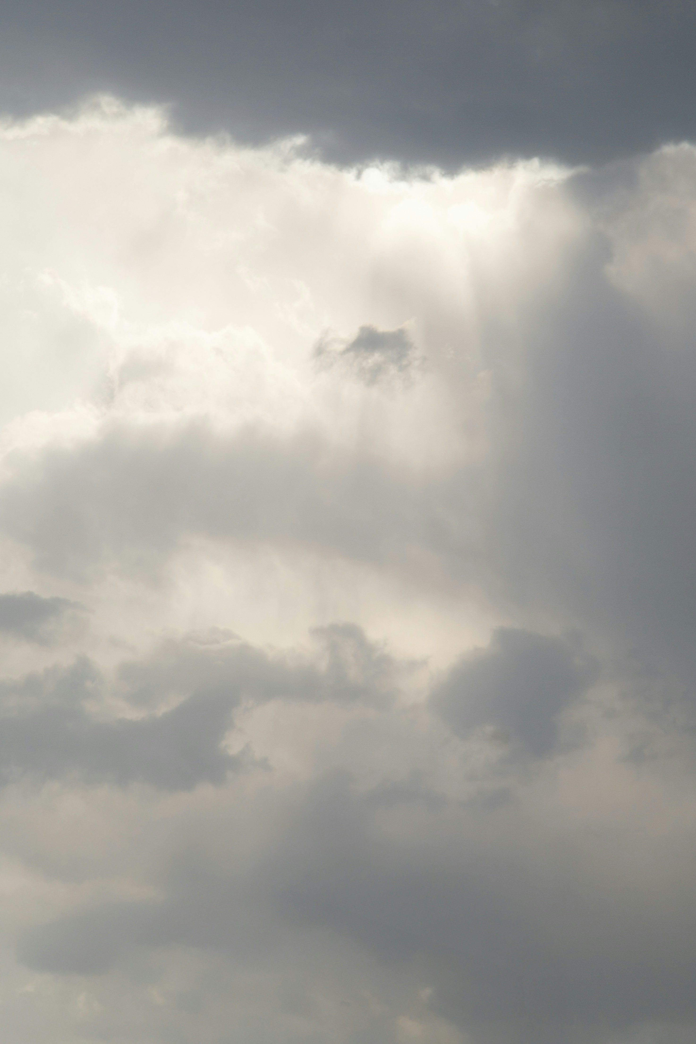 Soft rays of light breaking through a blanket of gray clouds, creating a serene and contemplative atmosphere.