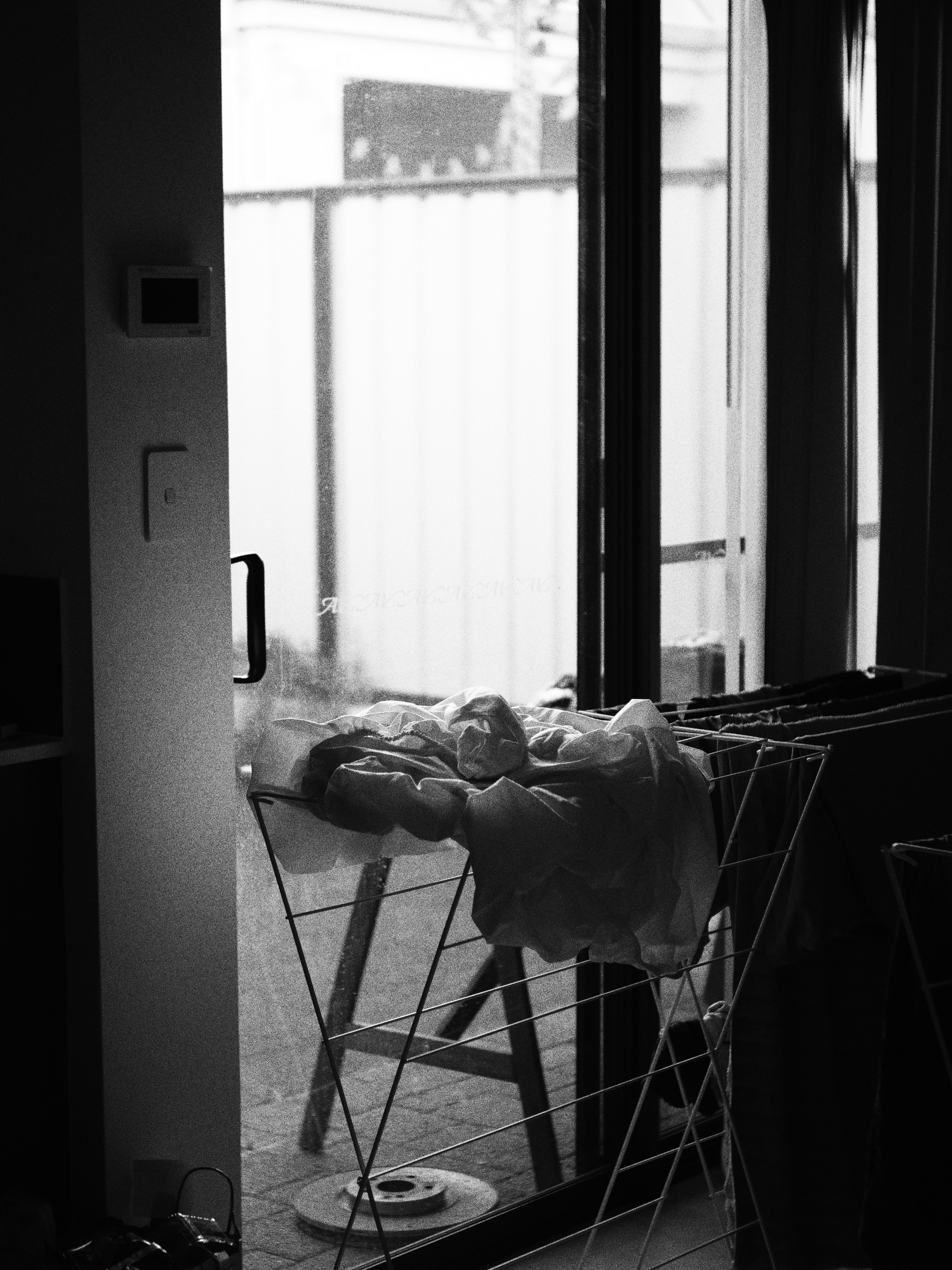 A laundry rack with crumpled clothes stands near a window, creating a serene atmosphere in a monochromatic setting.