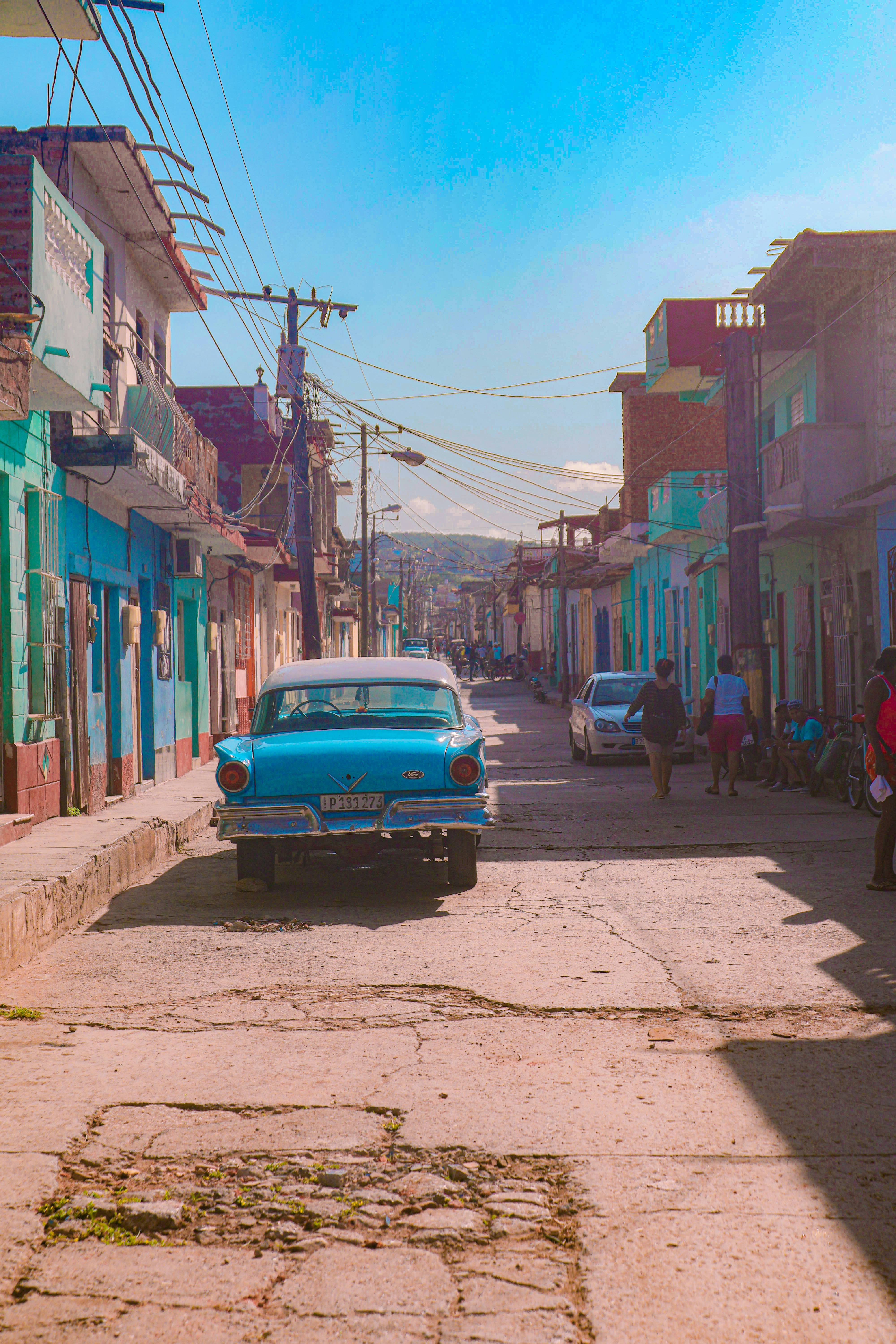 Classic blue car parked on a cobblestone street lined with vibrant buildings in a quaint neighborhood.