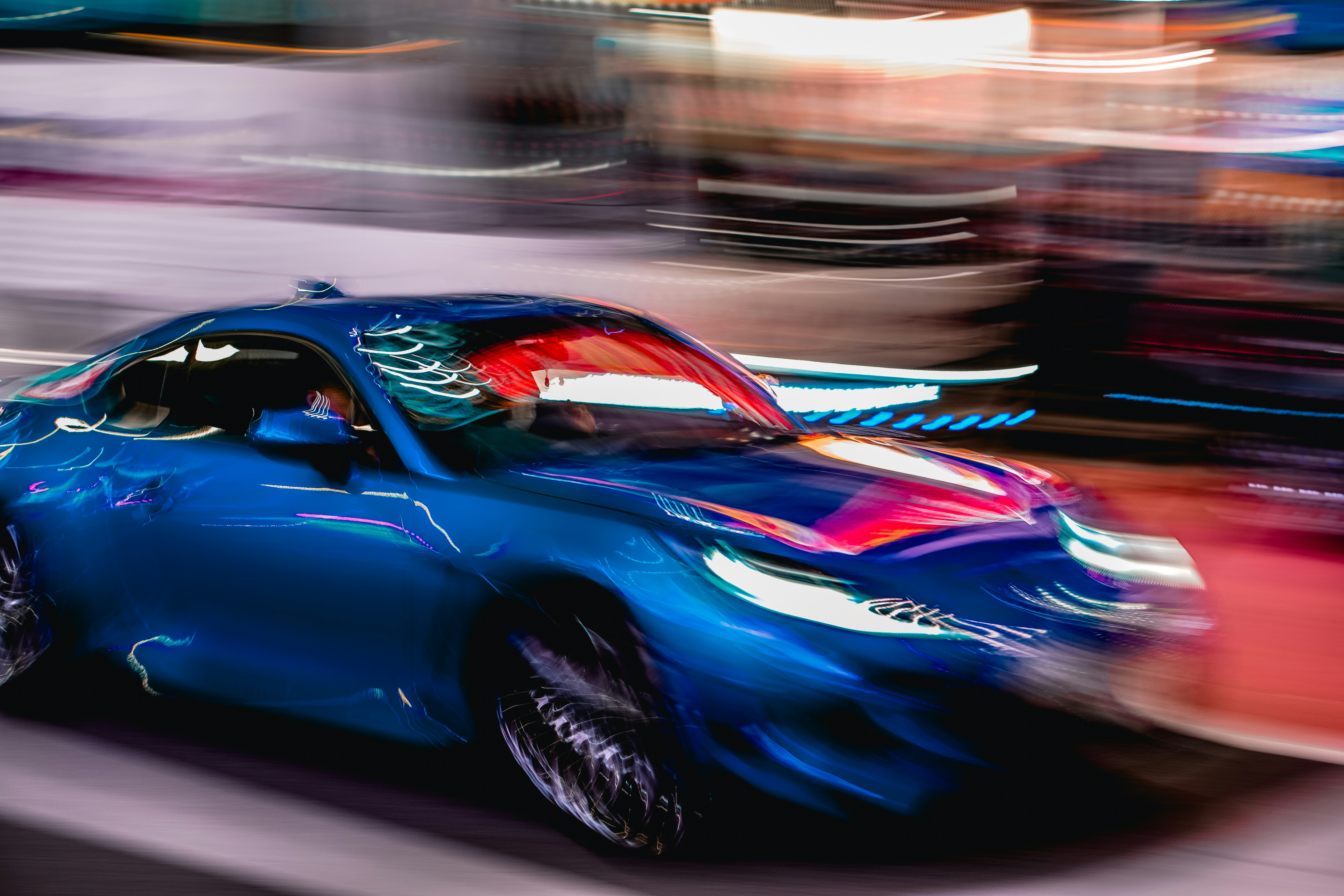 A blue car drives fast through city lights.