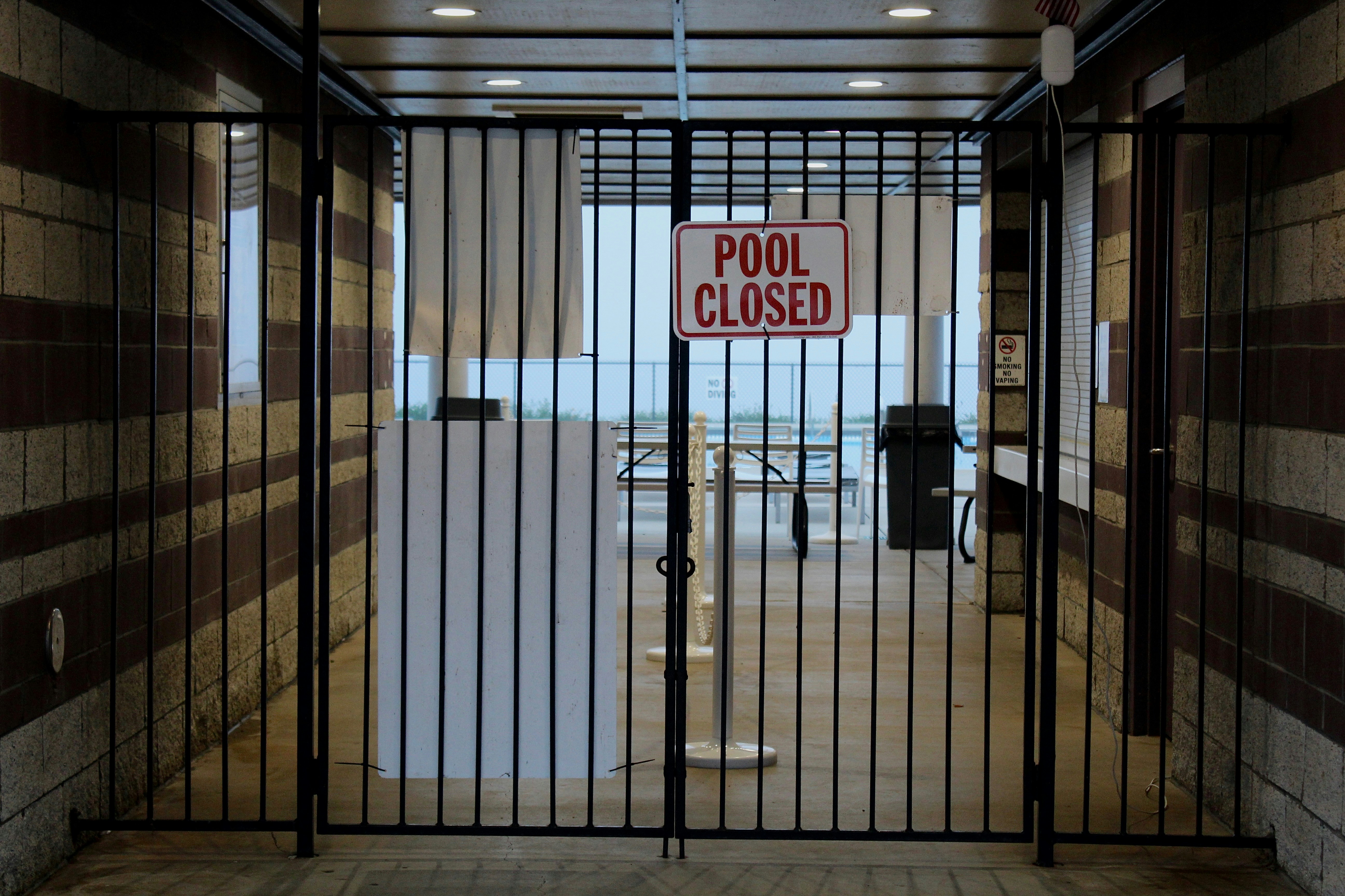 A gated entrance with a prominent 'POOL CLOSED' sign, indicating restricted access to the swimming area. The setting conveys a sense of abandonment and stillness.
