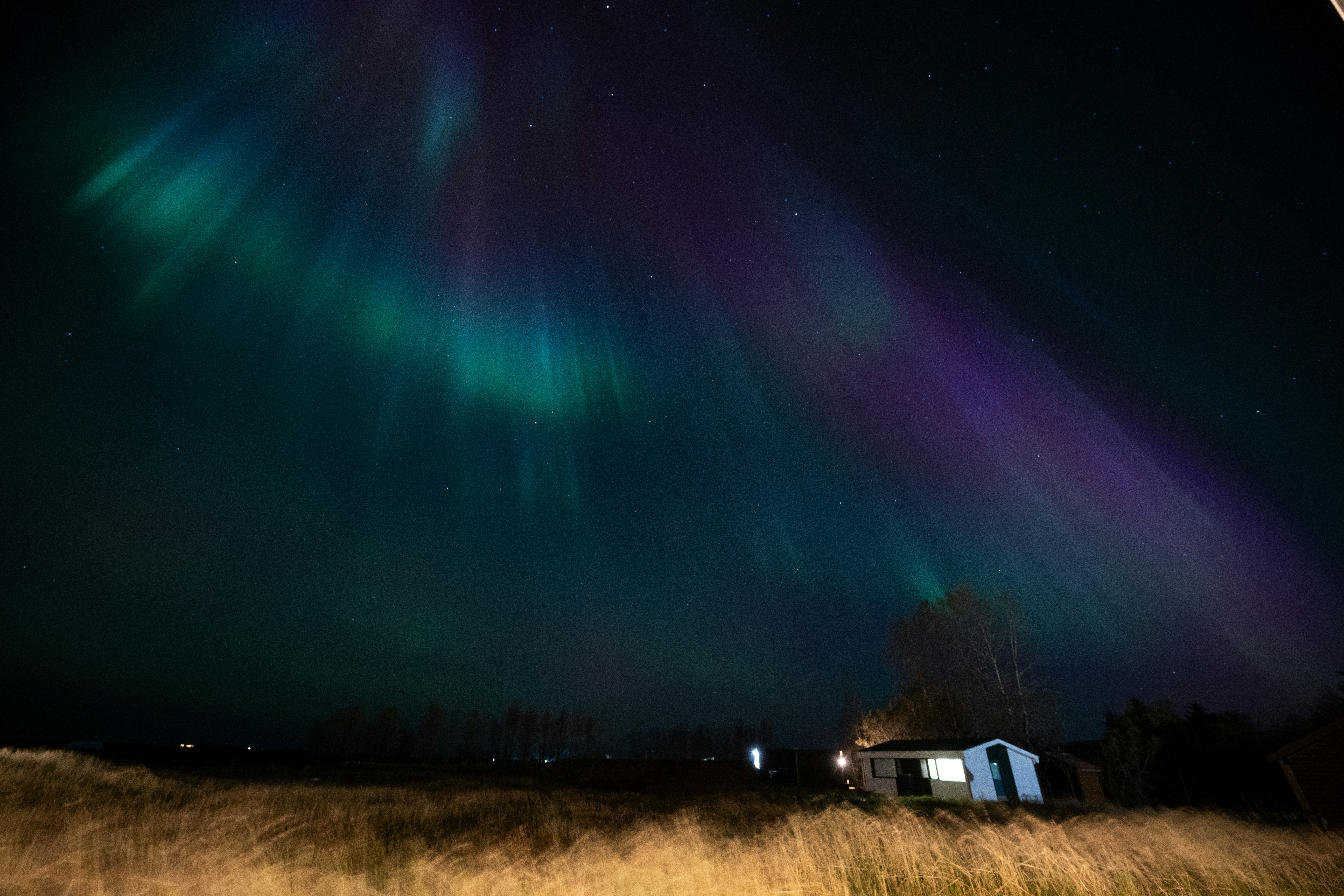 Vibrant auroras dance across the night sky, illuminating a serene landscape with a quaint cabin in the foreground. The scene captures the ethereal beauty of the northern lights.