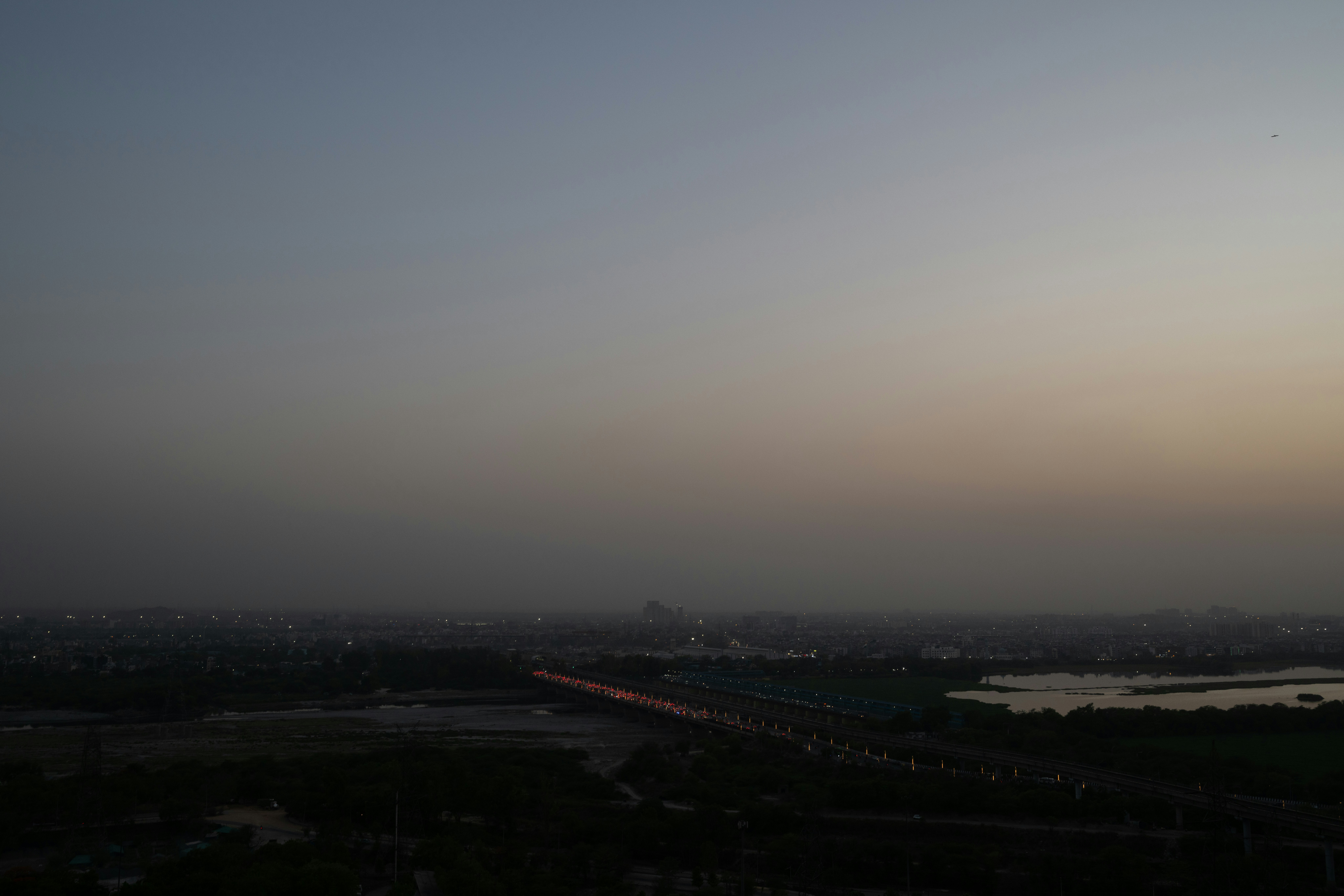 A tranquil evening view of a cityscape, showcasing a winding road illuminated by vehicle lights against a fading sky.