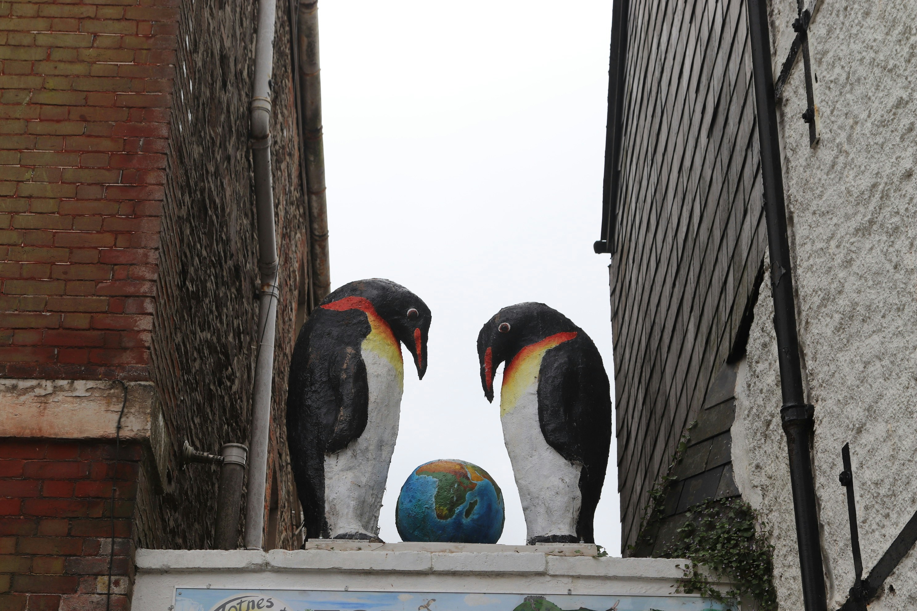 Penguin Sentinels Flank a Globe on a Rooftop Between Urban Walls