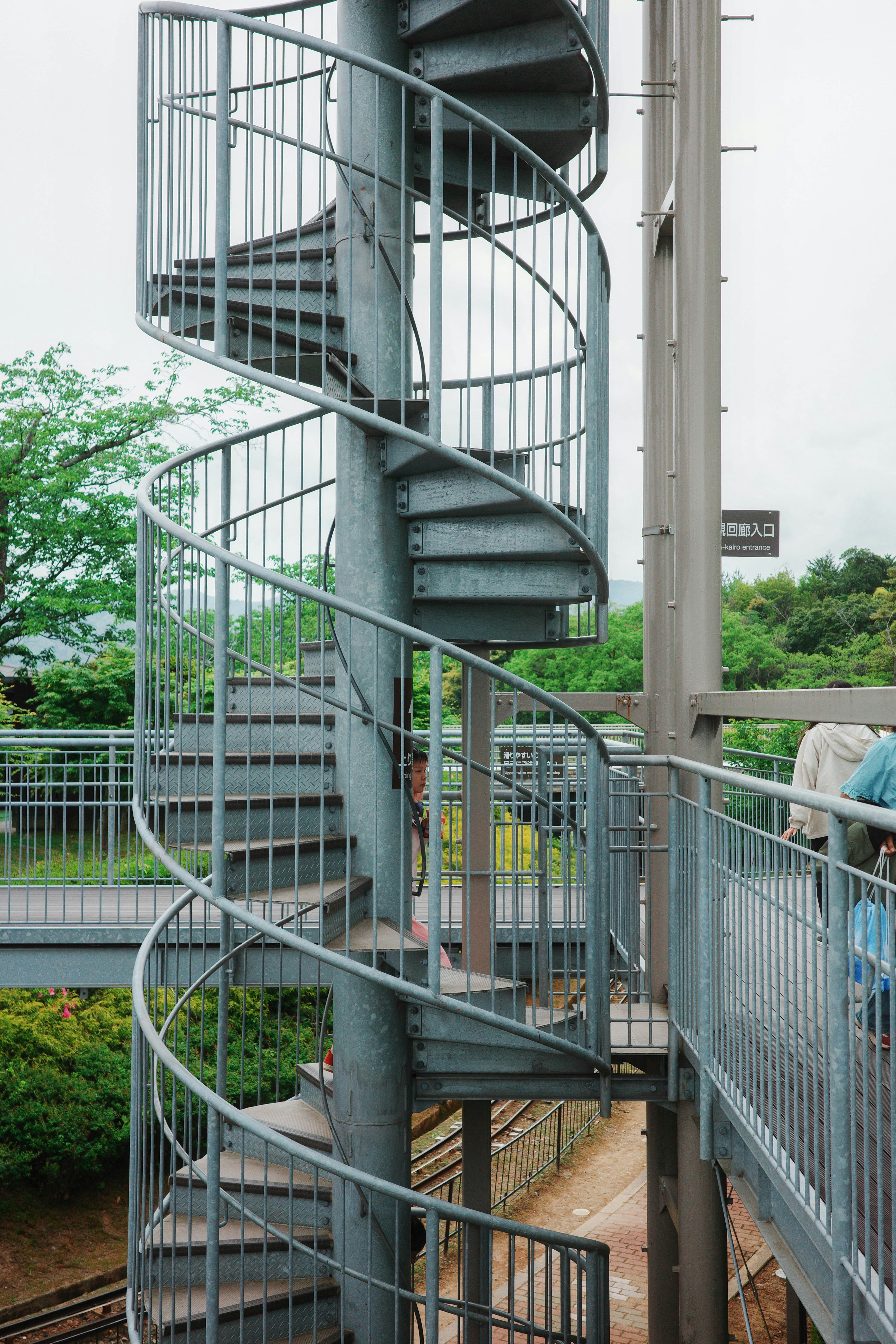 Metal spiral staircase leading upwards, surrounded by lush greenery and urban elements.