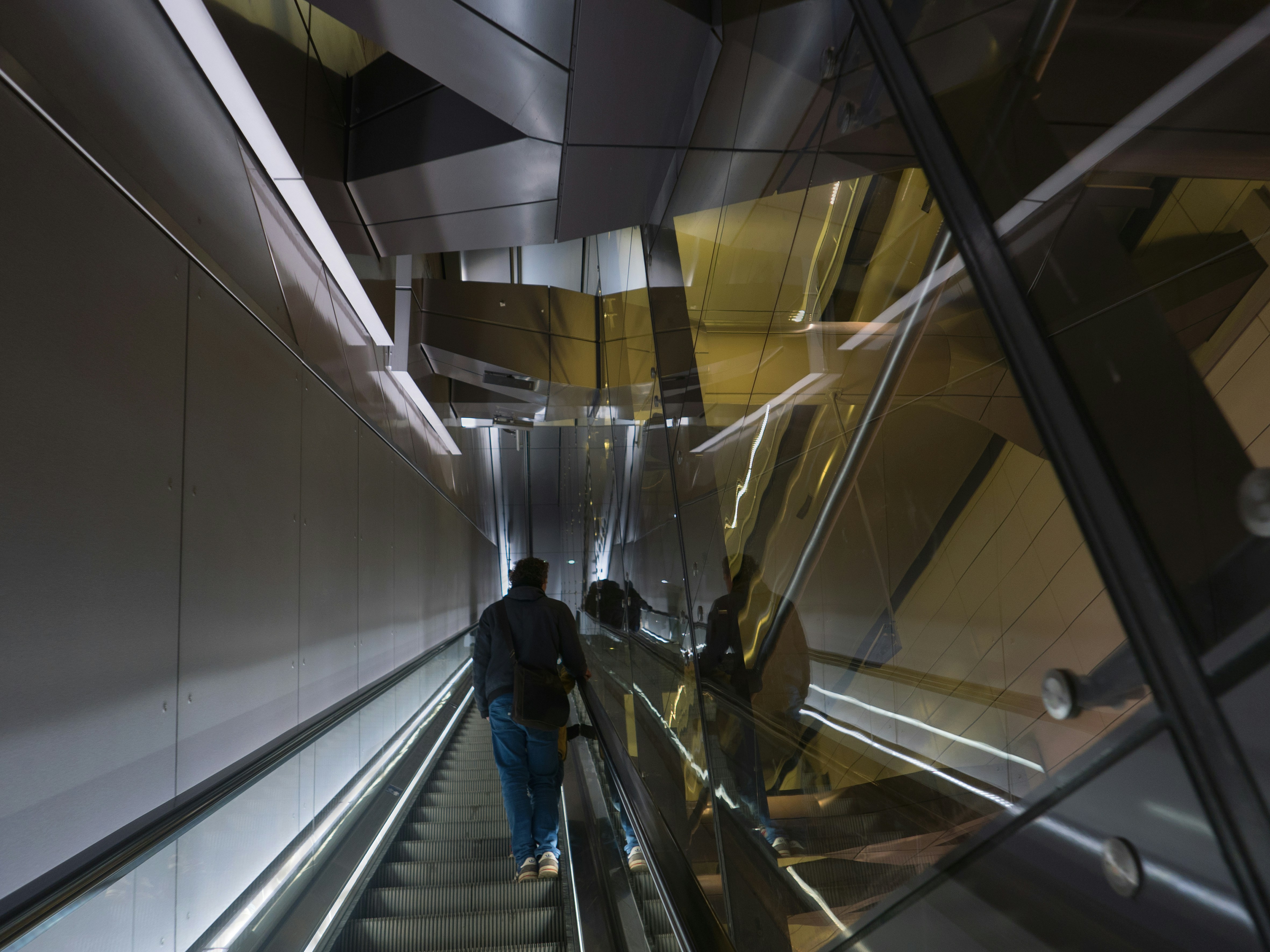 Free photo of a man on the long escalator, descending to the deepest platform of the metro Nort-South line in Amsterdam city. Modern urban architecture in grey ambient shades. Urban street photography of people in the cities of The Netherlands; free images by Fons Heijnsbroek, 2025 city wallpaper in free download. / Foto van een man op de roltrap in metrostation de Pijp, onder de Ferdinand Bolstraat. Hij gaat hier naar het diepste perron van de Noord-Zuidlijn. Straatfotografie in gratis download.