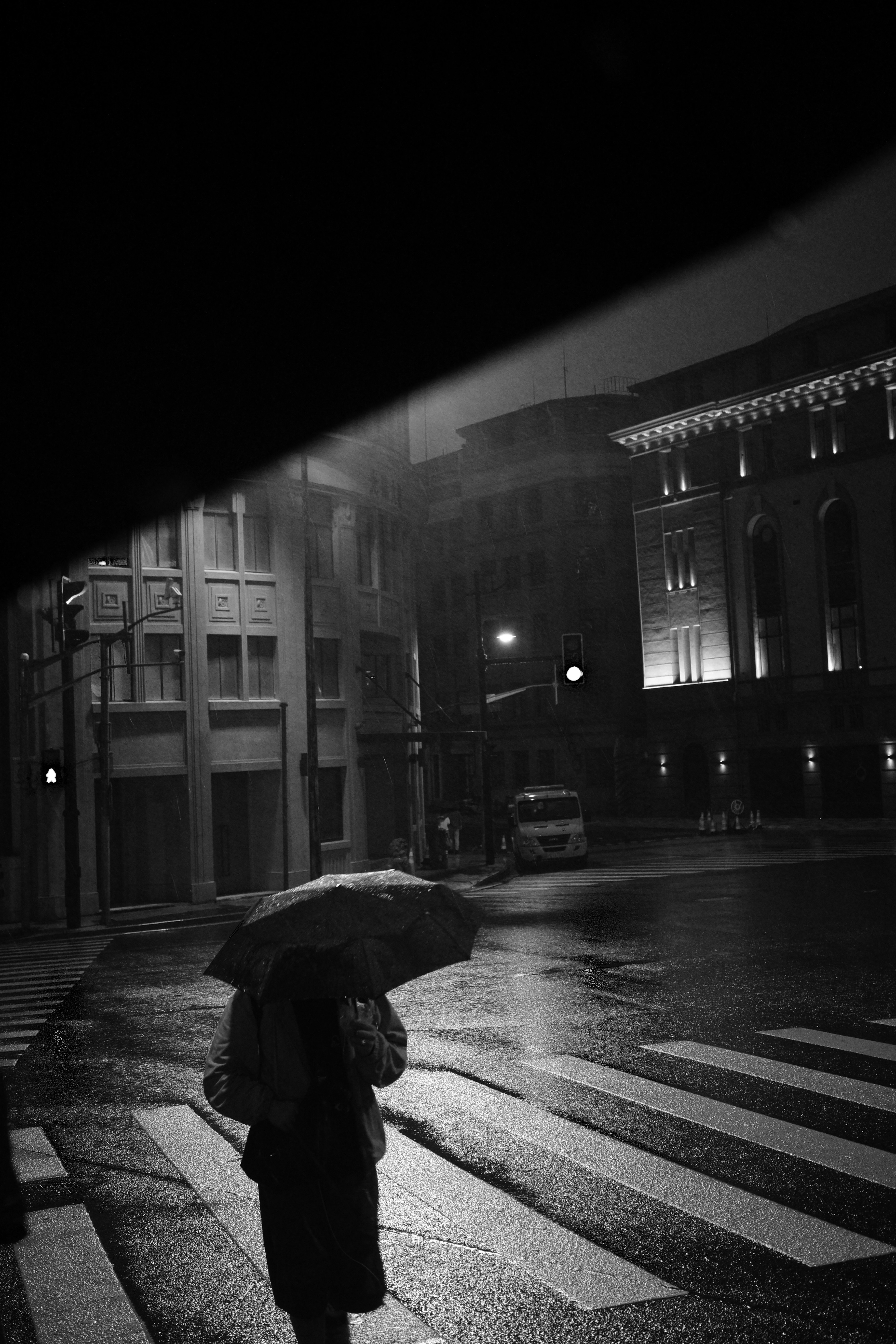 A person walks across a wet street under an umbrella.