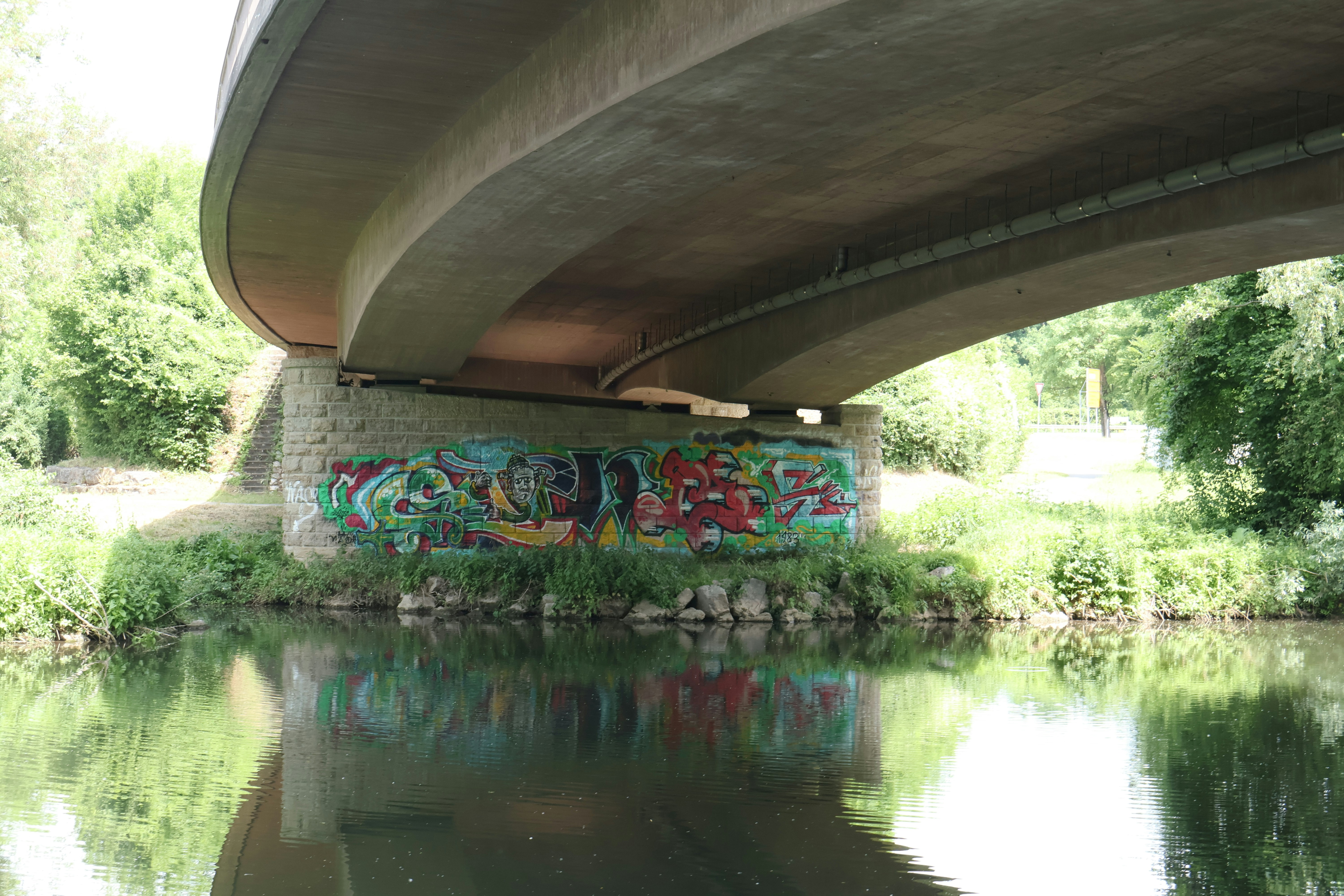 Graffiti below a bridge. | Graffiti adorns the bridge's underside over the river.
