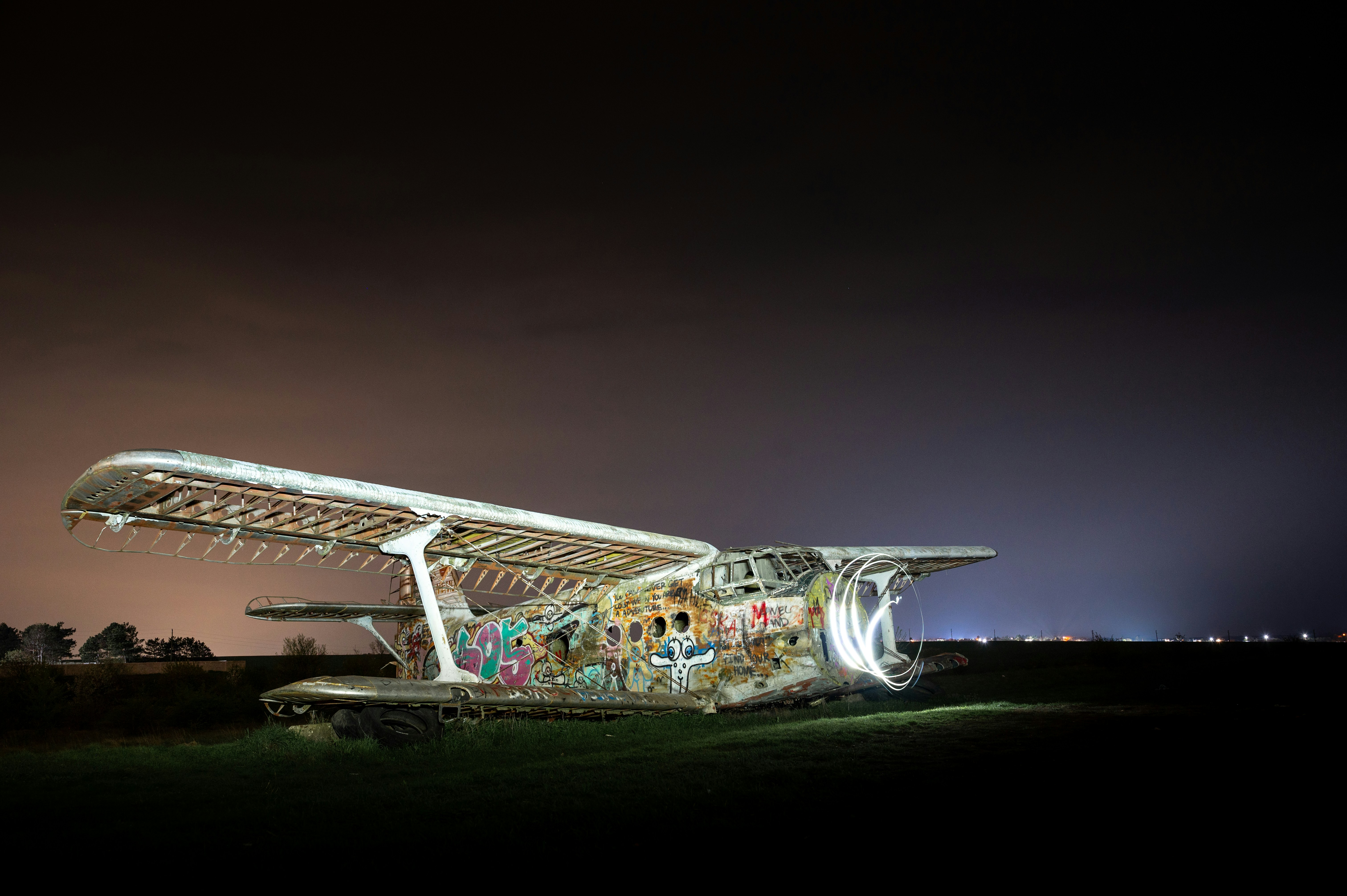 Abandoned airplane adorned with vibrant graffiti, illuminated against a dark night sky, showcasing urban decay and artistic expression.