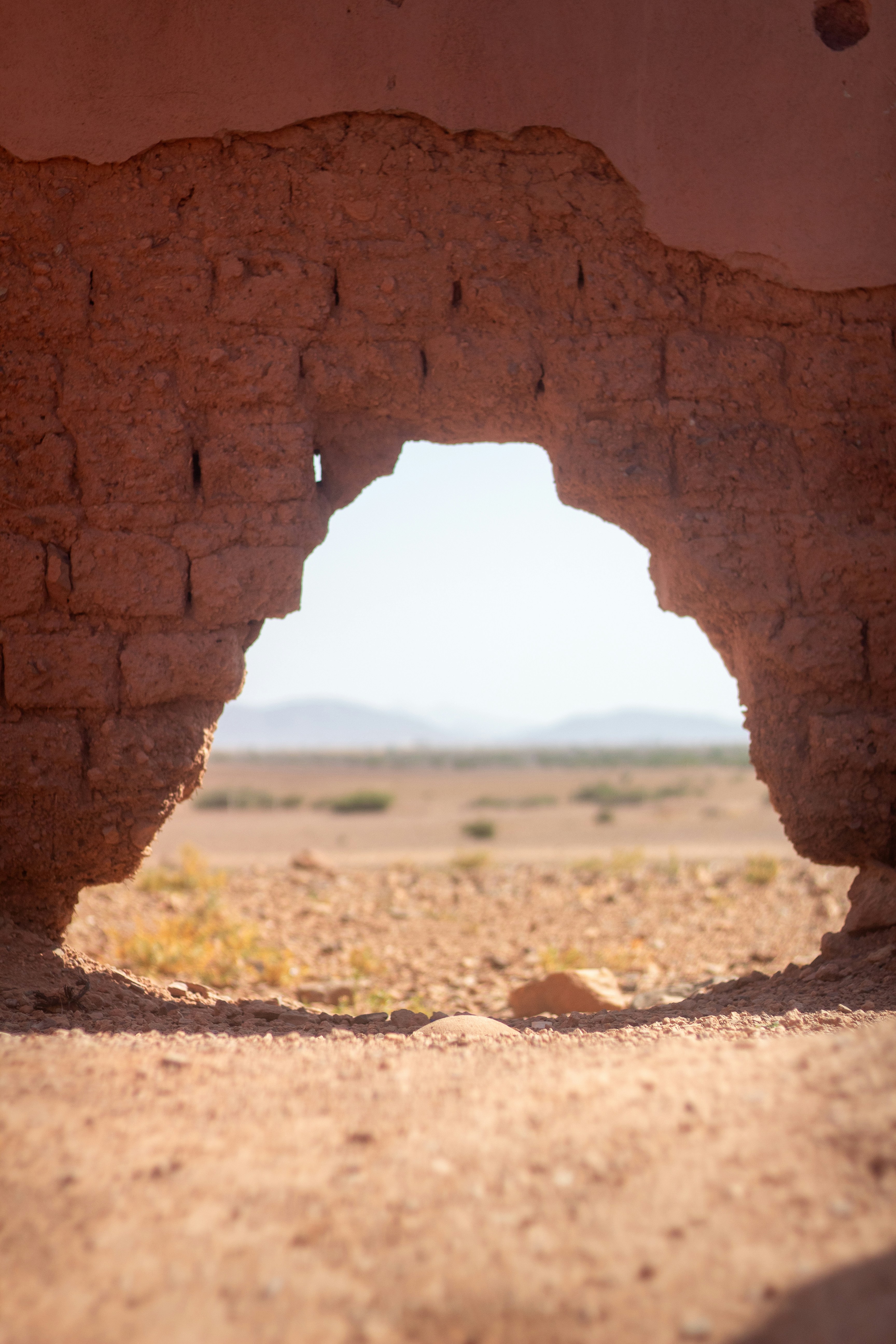 A weathered stone wall with a jagged opening reveals a vast desert landscape beyond, highlighting the contrast between man-made structures and natural beauty.