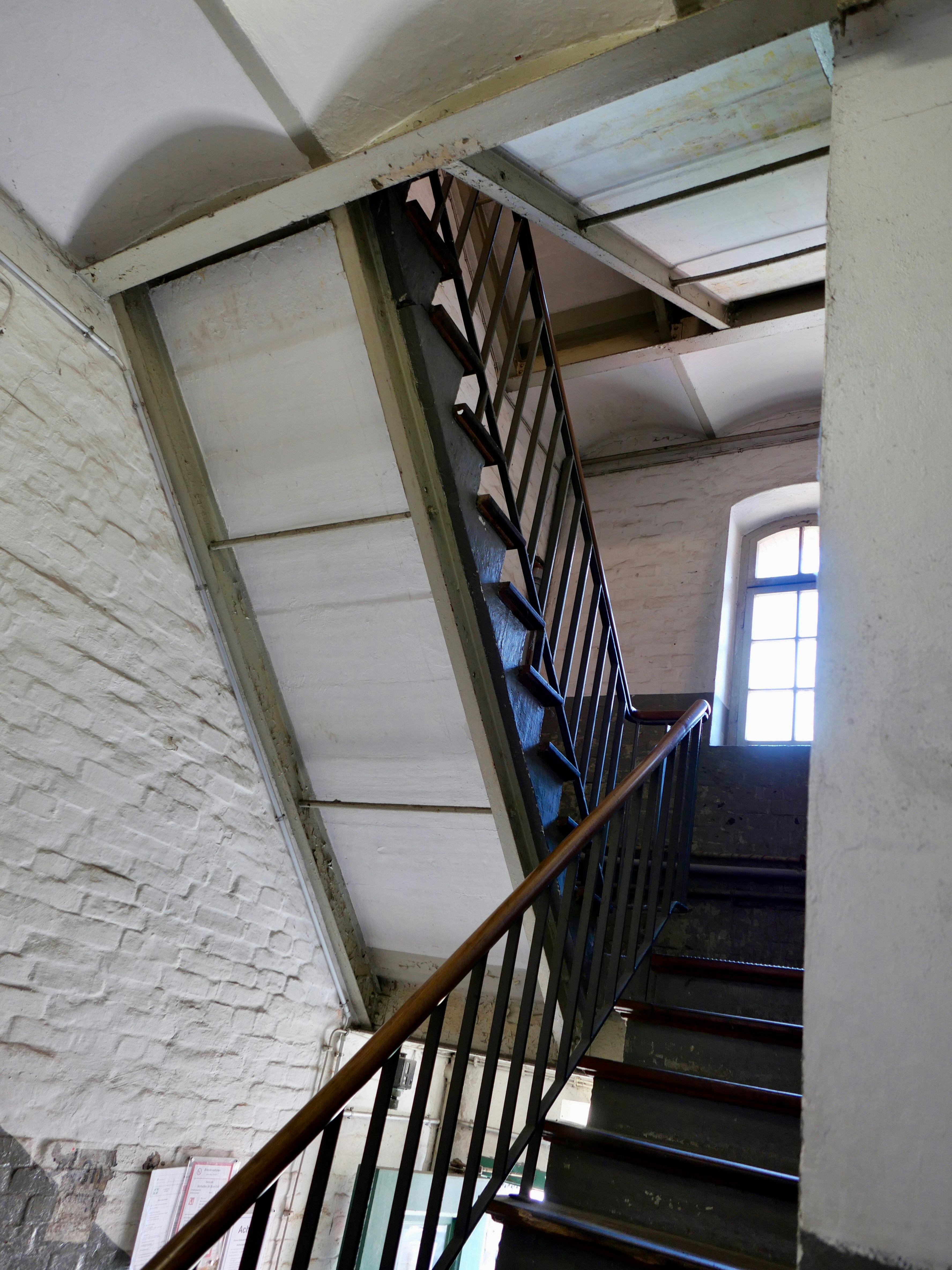 Industrial staircase leading upward, illuminated by natural light filtering through a window at the top.