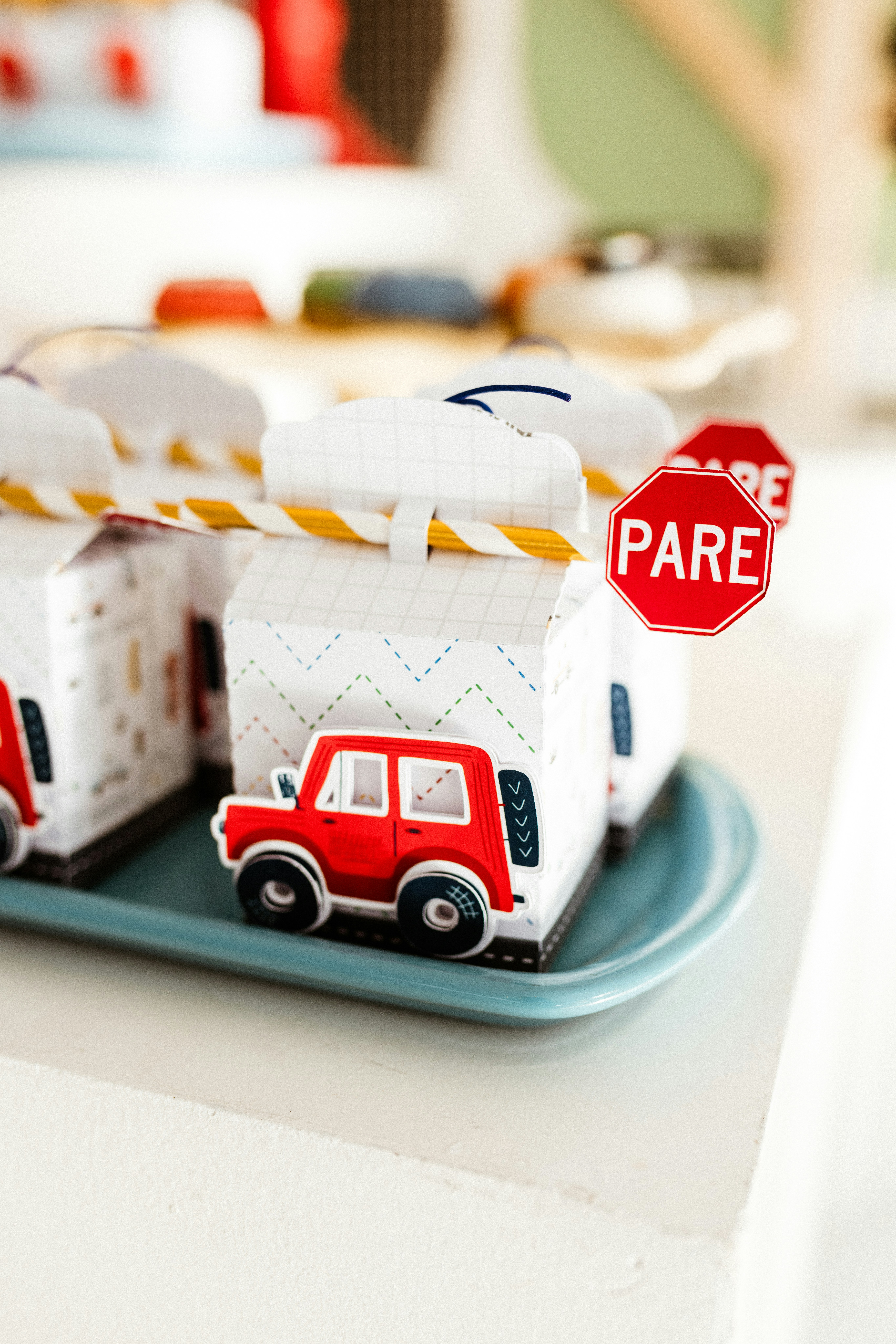 Colorful toy cars and snack boxes arranged on a blue tray, featuring a playful stop sign labeled 'PARE.'