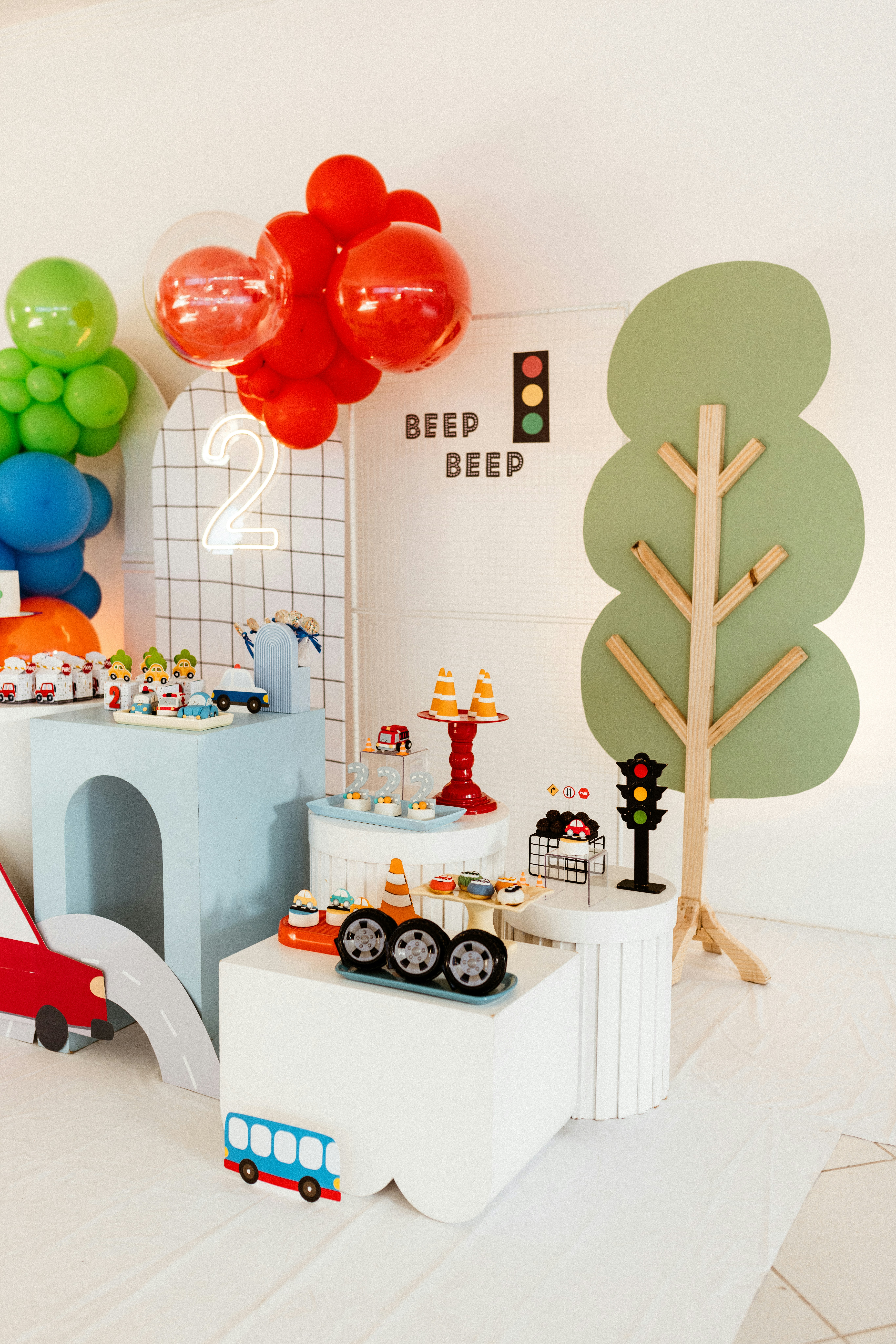 Colorful party decor featuring traffic-themed elements, including toy vehicles and a vibrant balloon arrangement. The scene is designed for a child's birthday celebration.