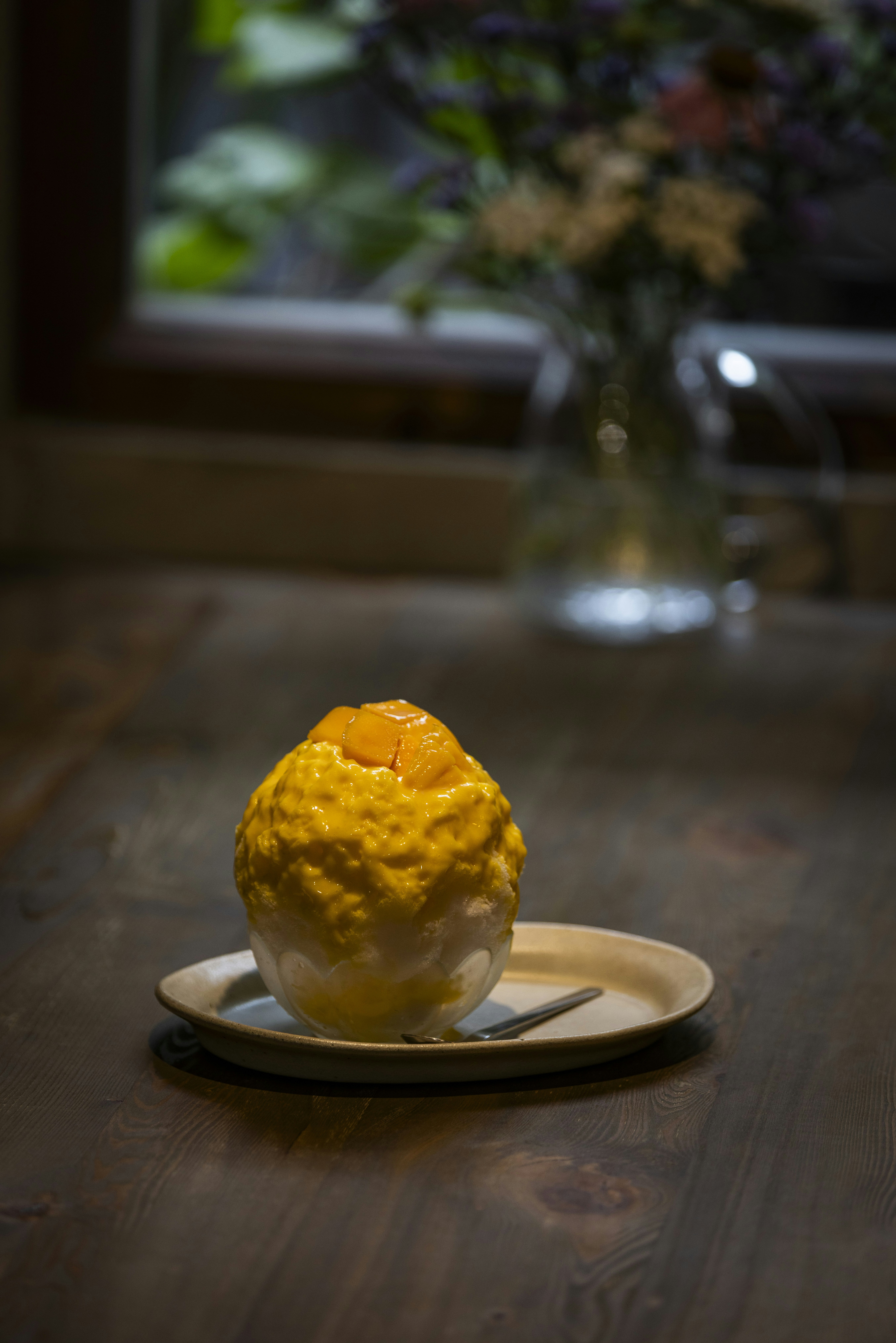 A beautifully crafted dessert featuring a mound of mango-flavored shaved ice topped with bright orange mango pieces on a simple plate.