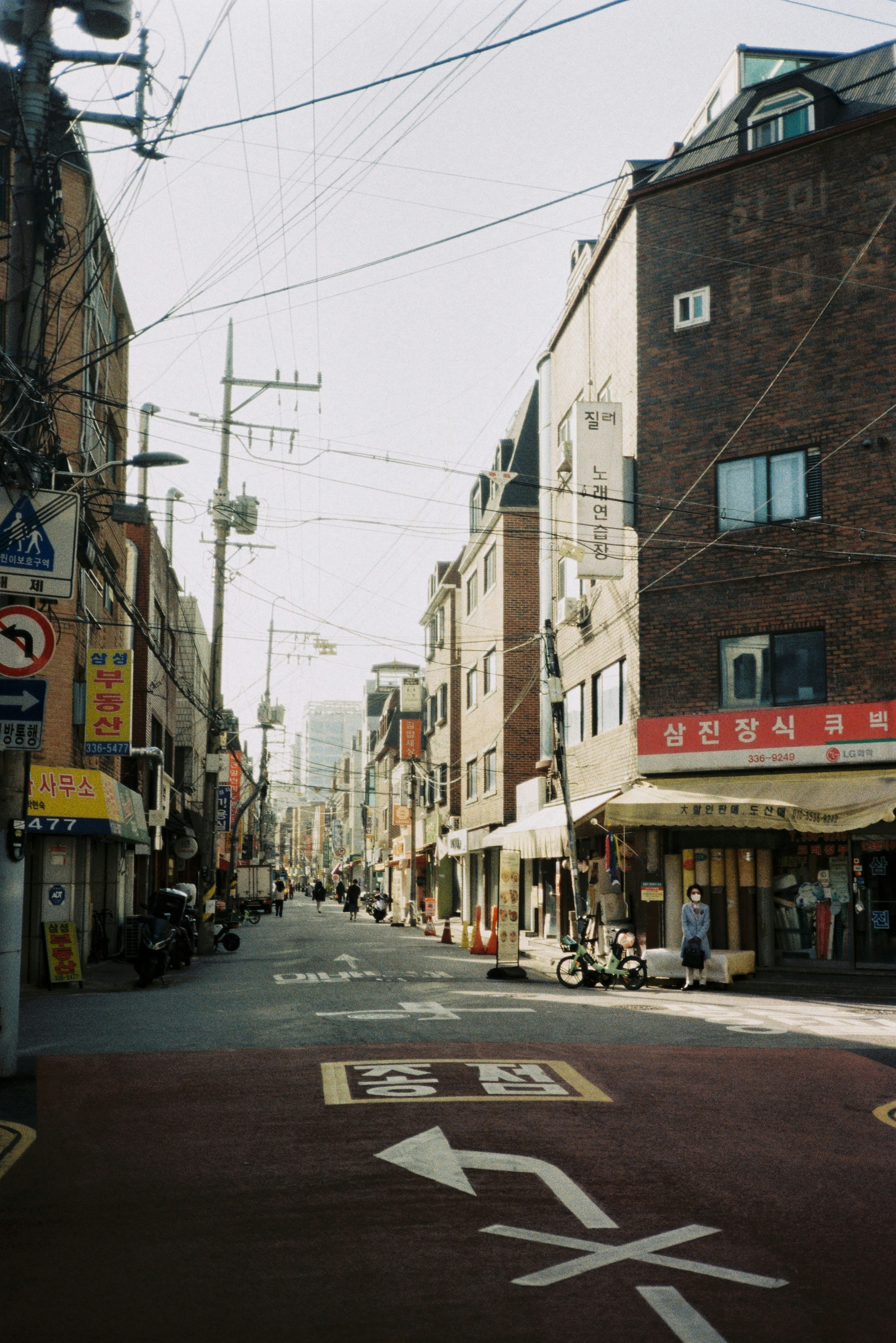 A bustling street scene featuring shops and power lines in a lively urban environment. The composition highlights the everyday life and architecture of the area.