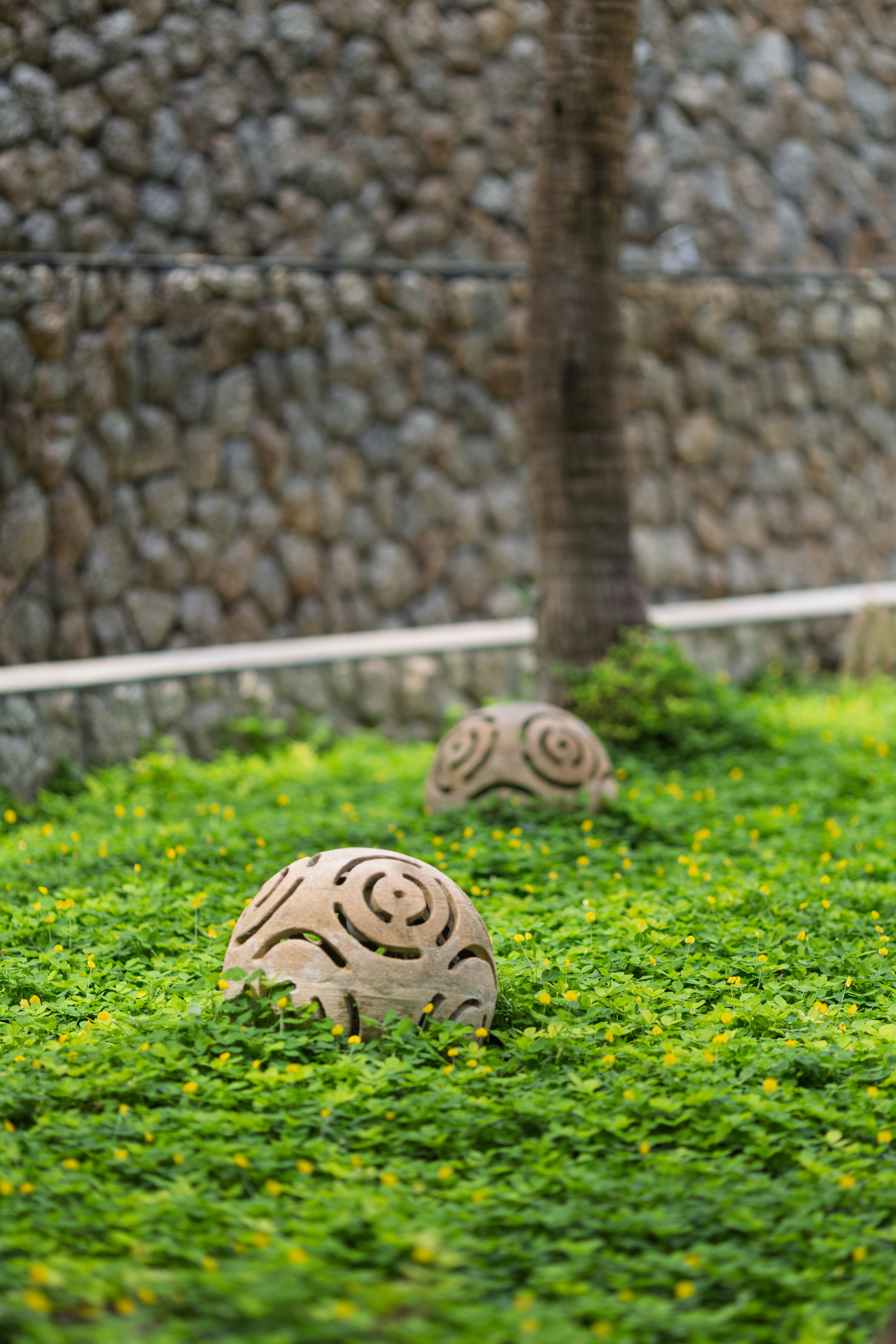 Decorative stone spheres nestled among vibrant green foliage and yellow flowers in a serene garden setting.