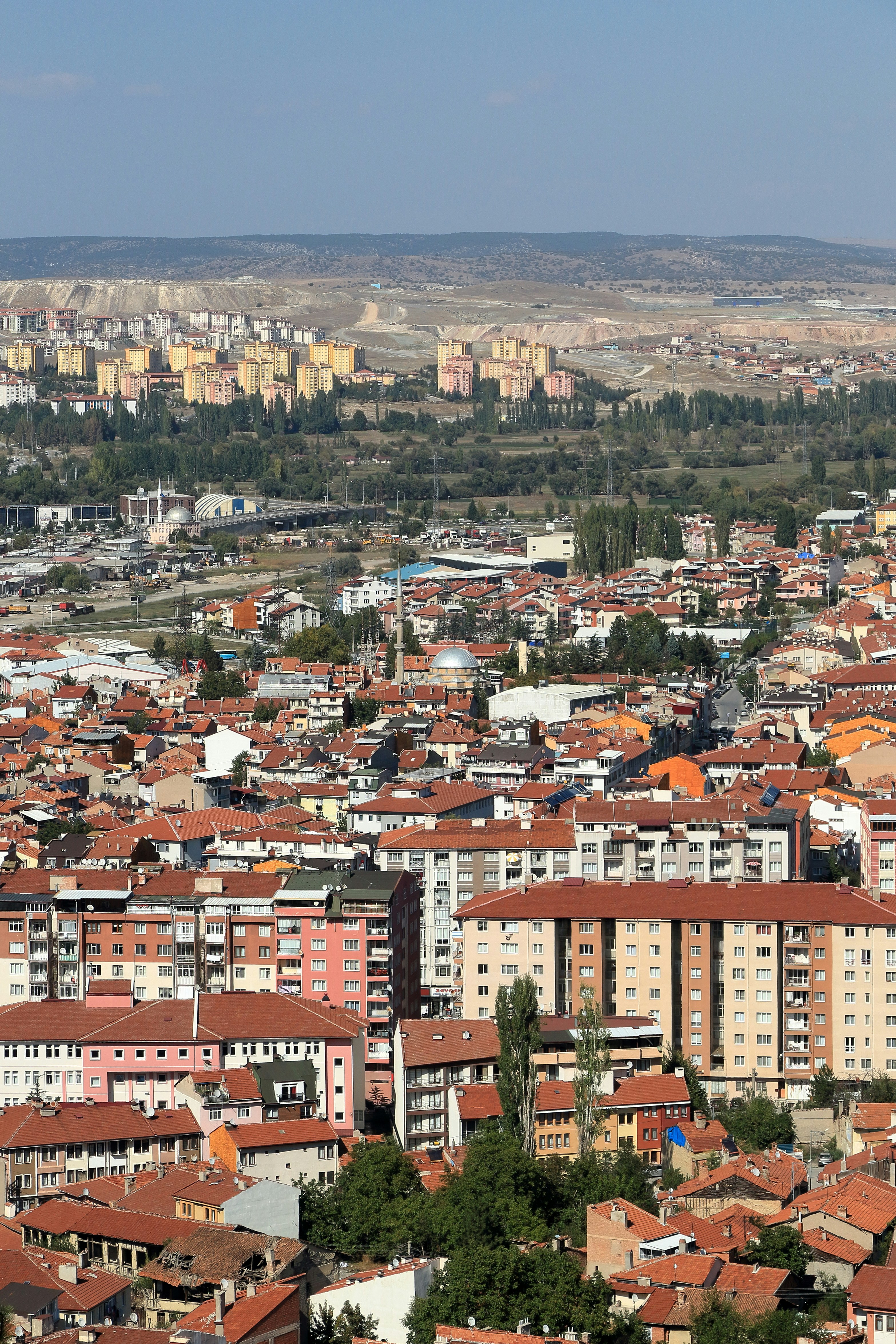 Vast cityscape showcasing a dense arrangement of colorful rooftops and buildings, with a backdrop of rolling hills and distant structures.