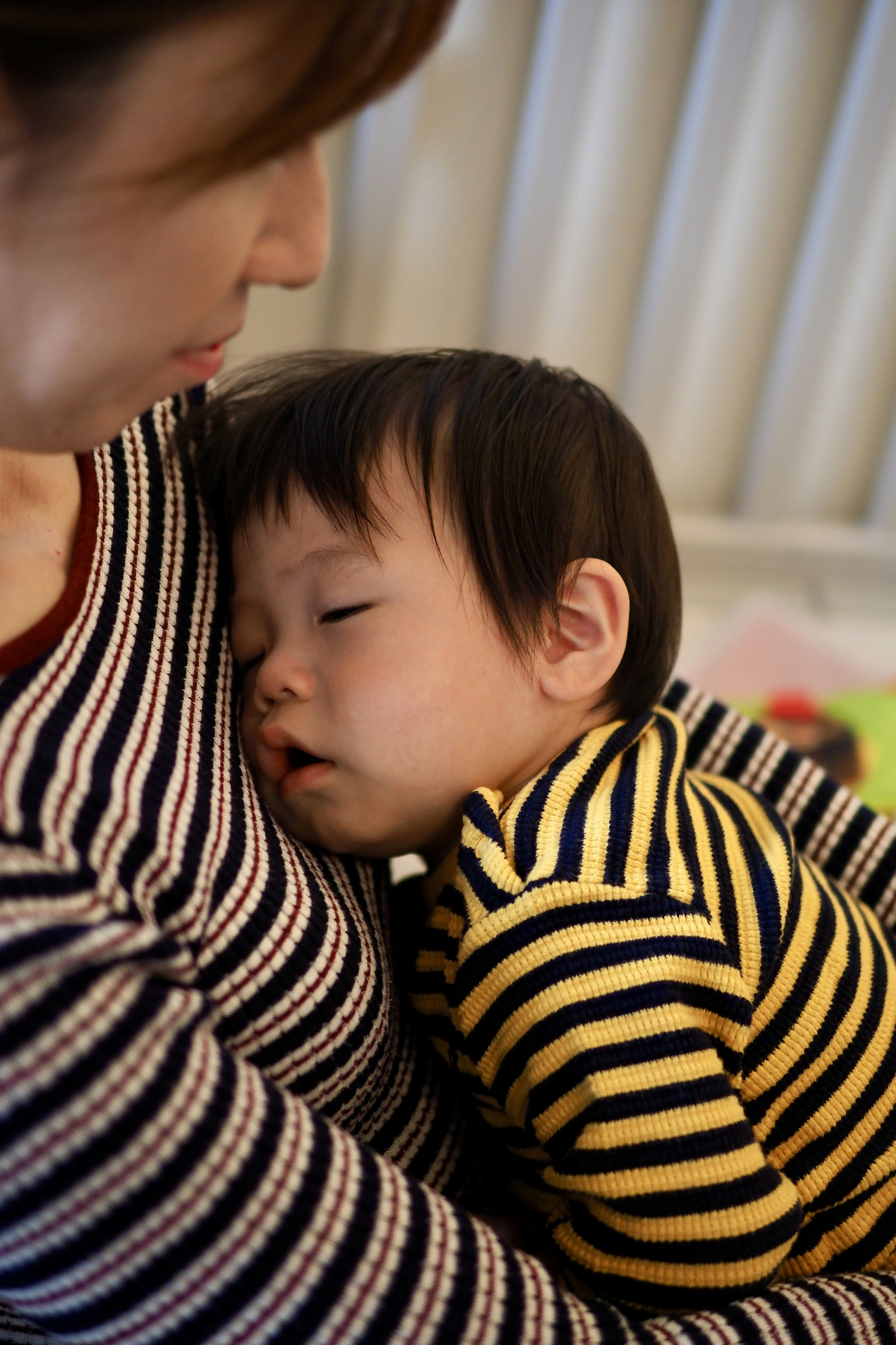 A sleeping child nestled against a caregiver, showcasing a moment of tenderness and comfort. The soft textures and warm colors enhance the intimate atmosphere.