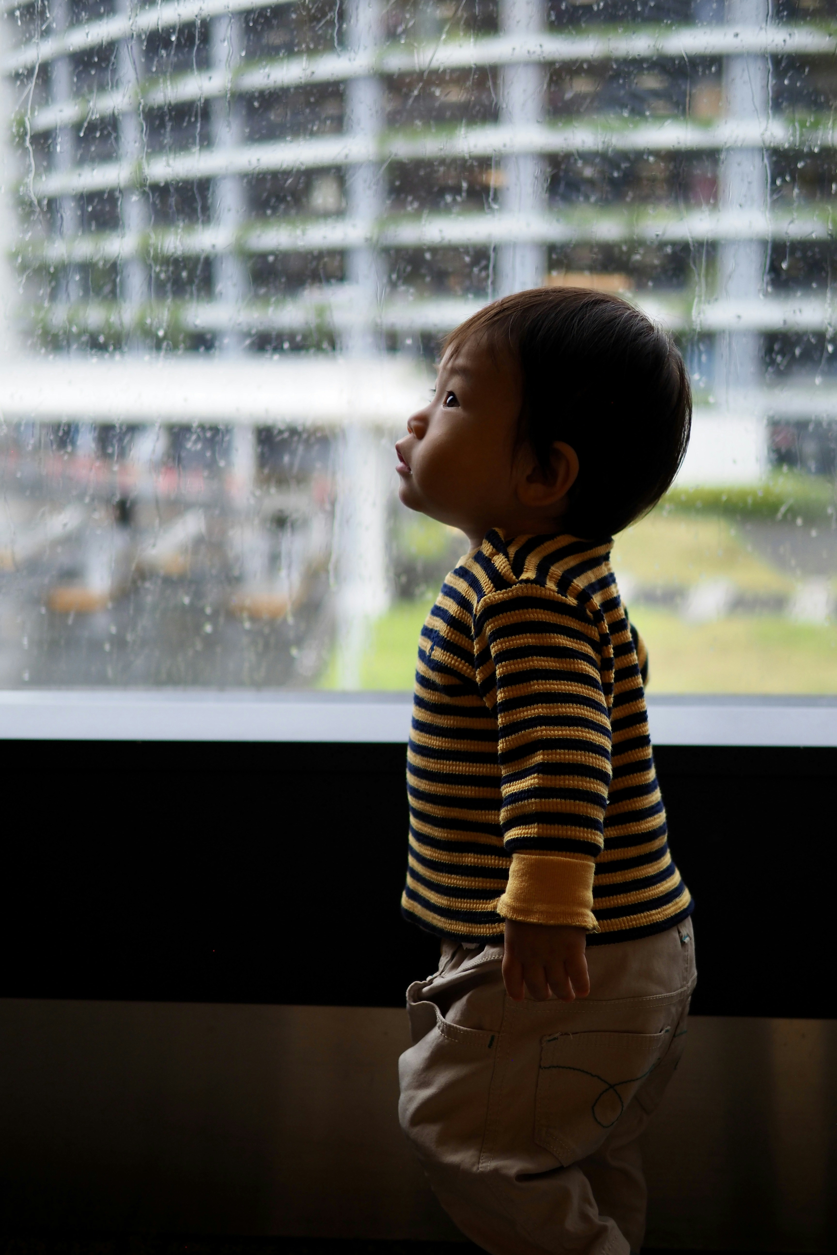 A baby looks out of a rainy window.