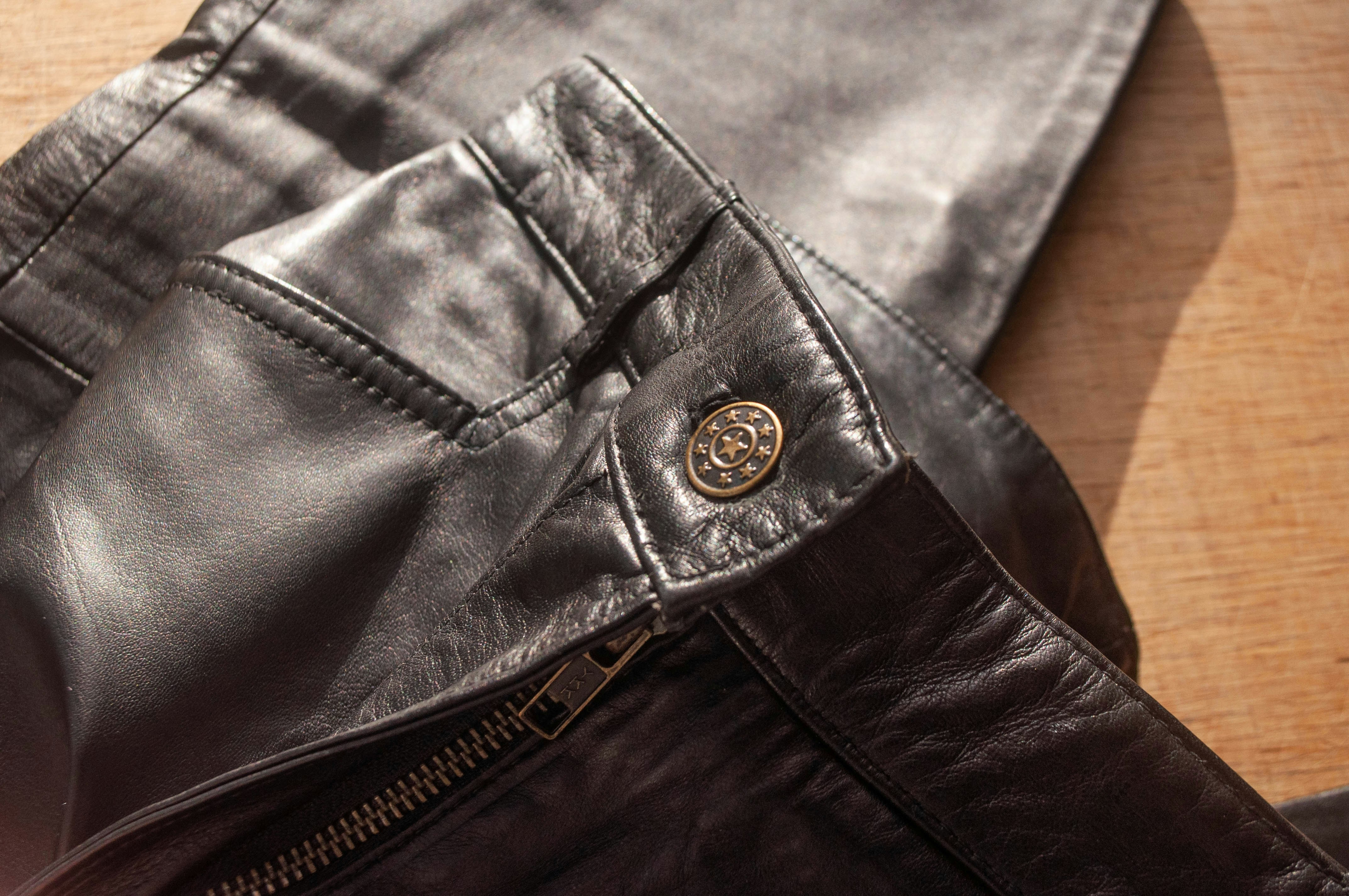 Close-up of a black leather garment showcasing intricate stitching and a decorative button. The texture highlights the quality and craftsmanship of the material.