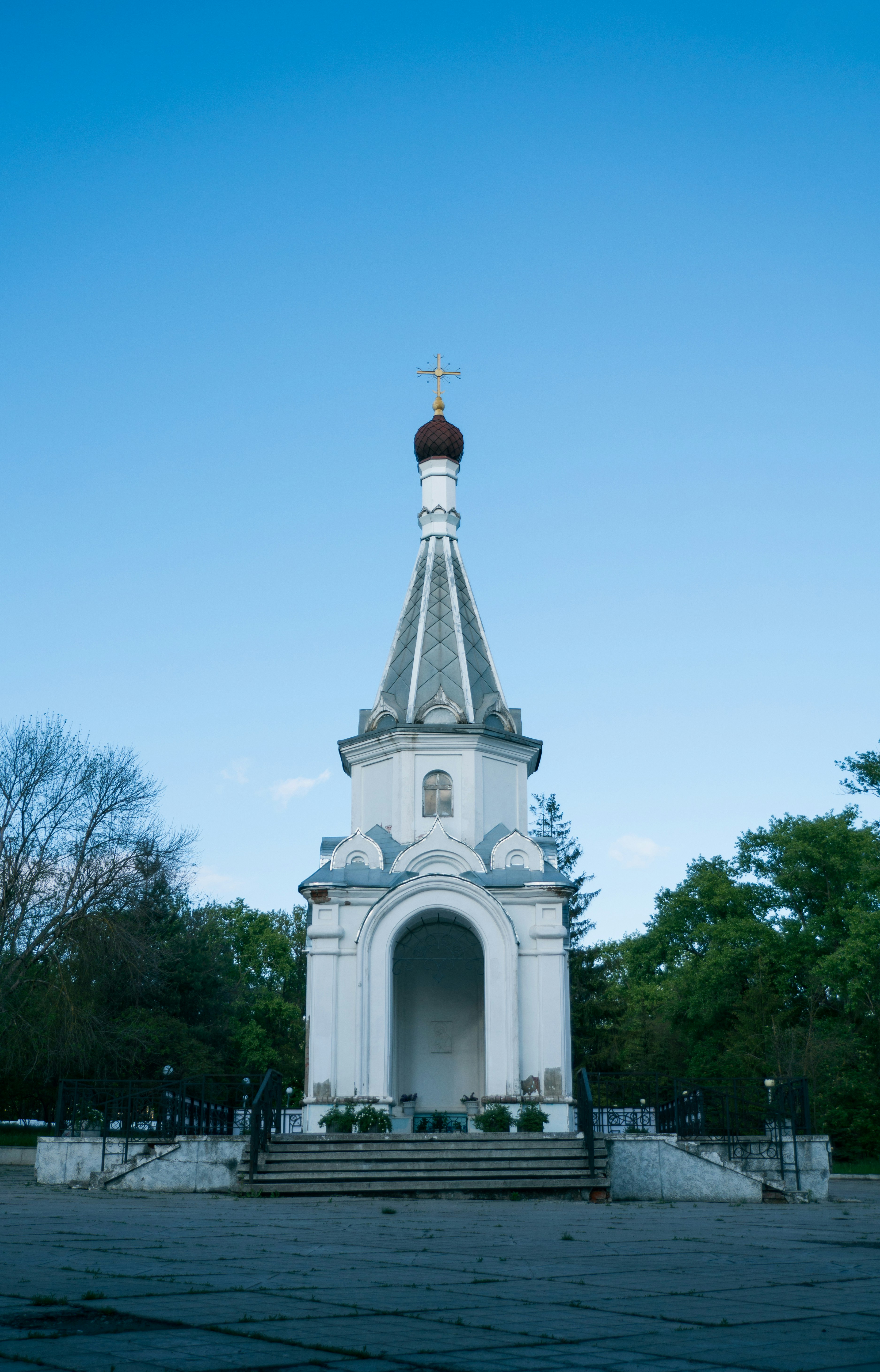 A view of the church bell tower from behind the trees, set against a sunset sky.