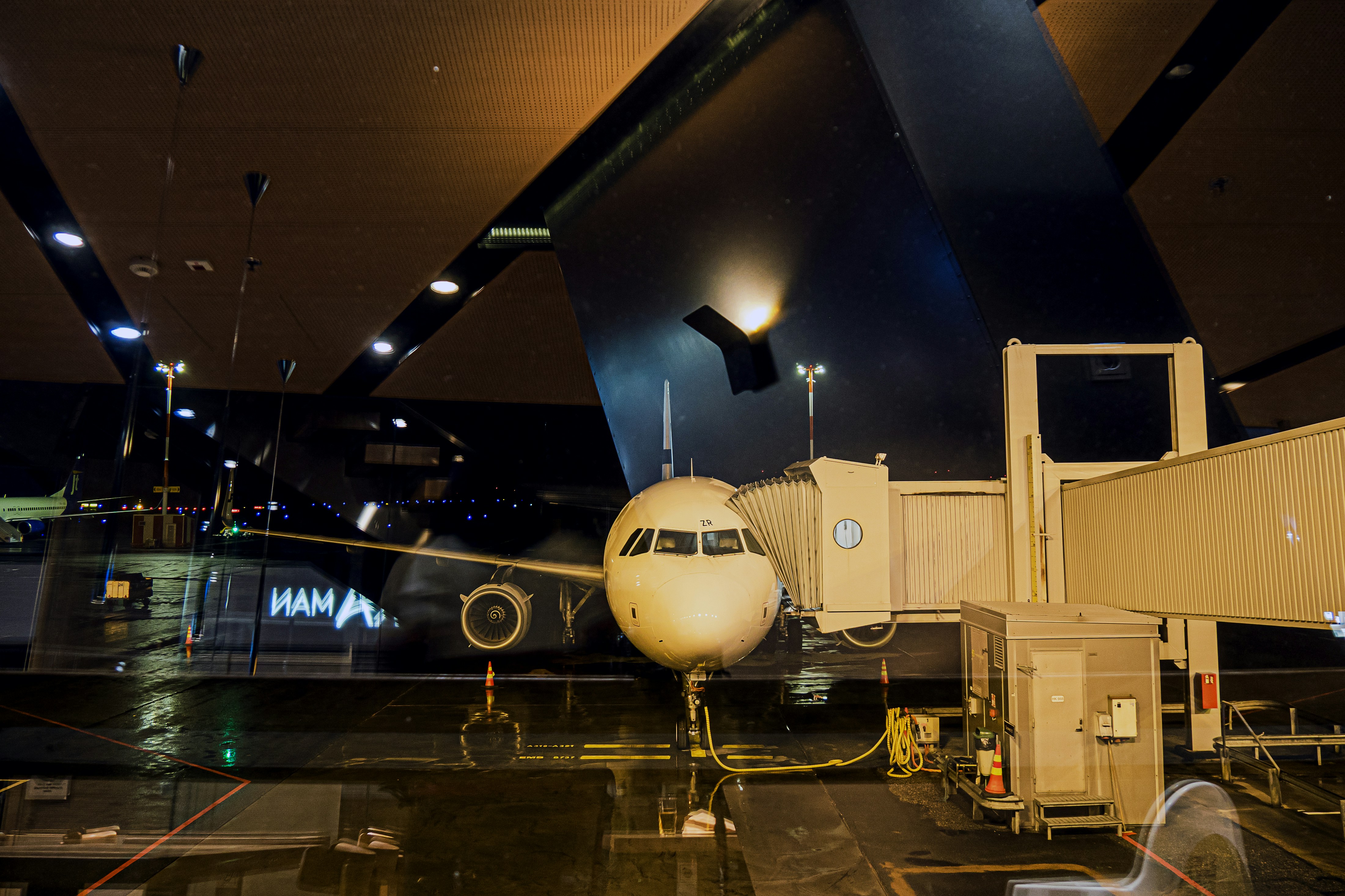 Airplane docked at a terminal gate, illuminated by ambient lighting, with reflections creating a layered visual effect.