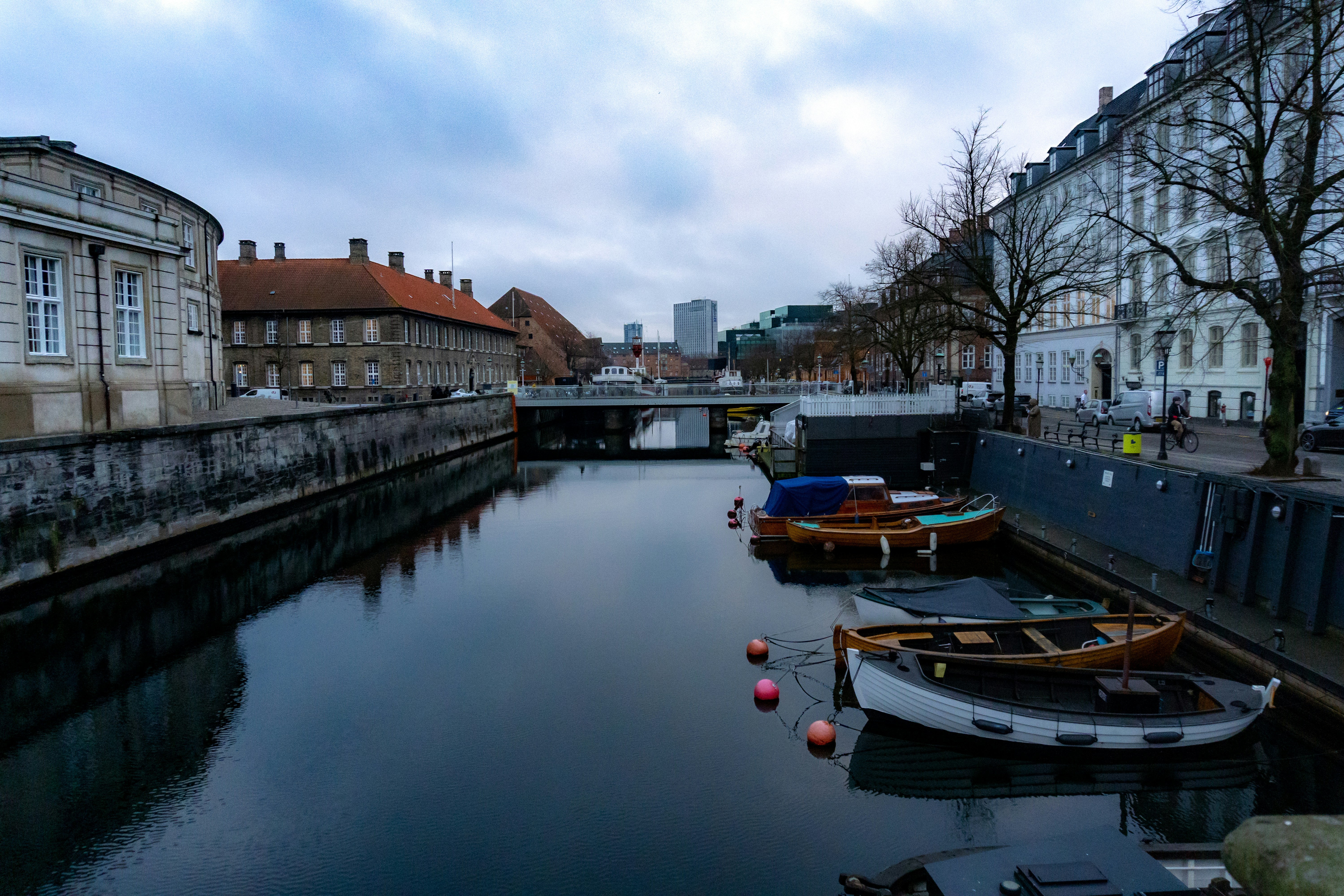 Calm canal scene featuring moored boats and historic buildings along the waterway. Soft light enhances the tranquil atmosphere.