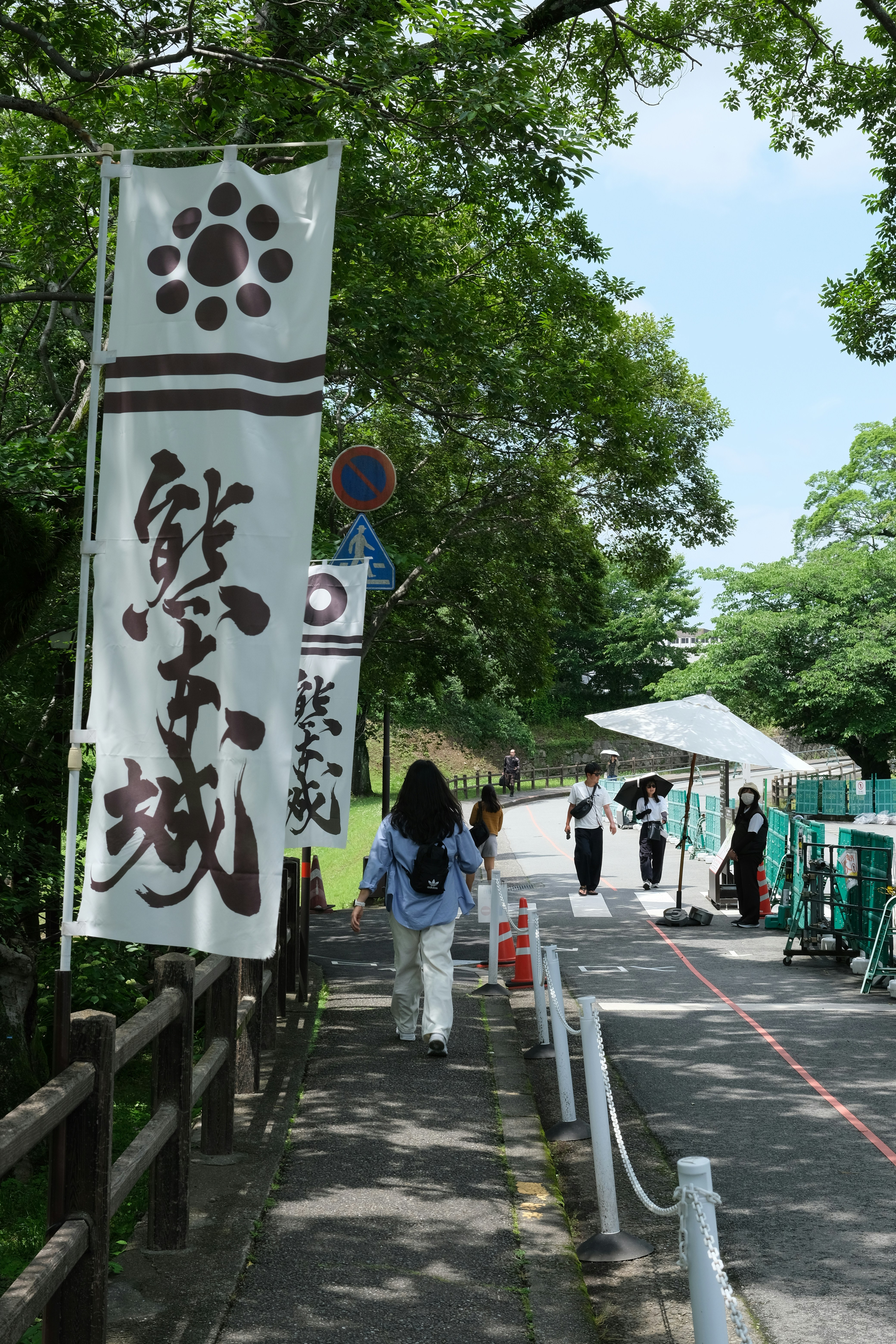 Visitors stroll along a tree-lined path, passing traditional banners that hint at local history and culture.