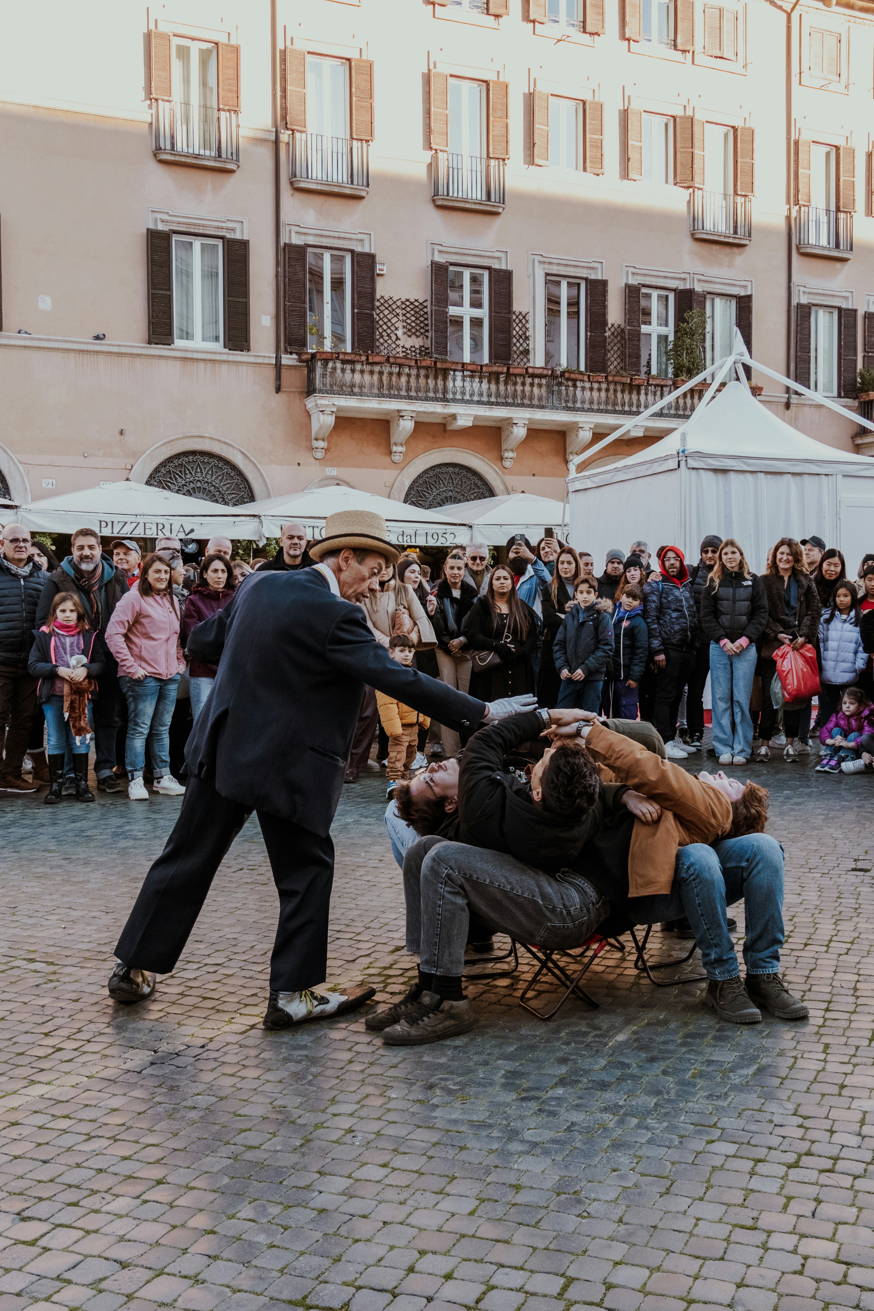 Street performers engage an audience in a captivating display of balance and coordination in a bustling plaza. The scene captures the energy and interaction of the performers and the crowd.