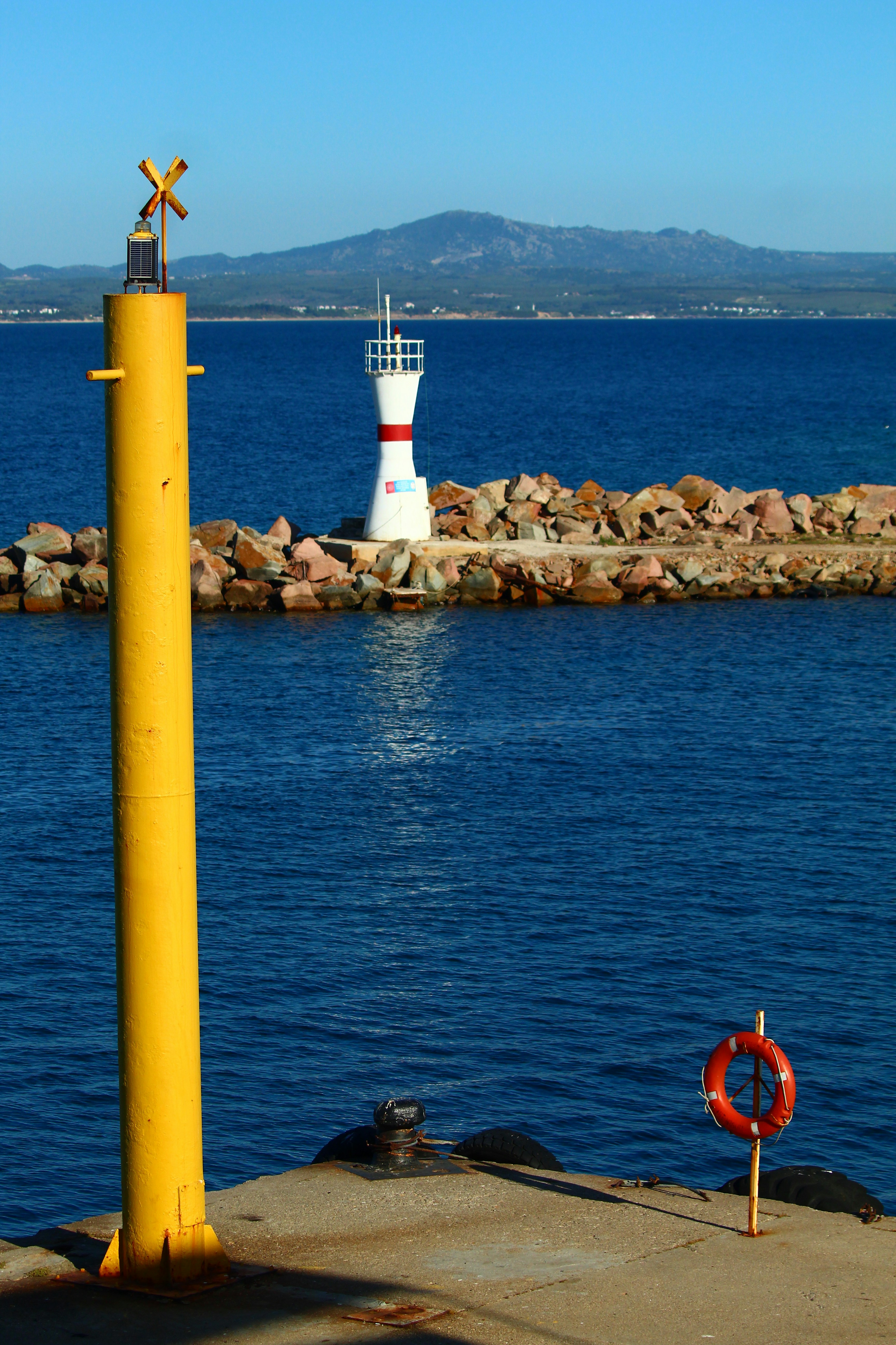 White Lighthouse with Red Bands Guards a Quiet Blue Harbor