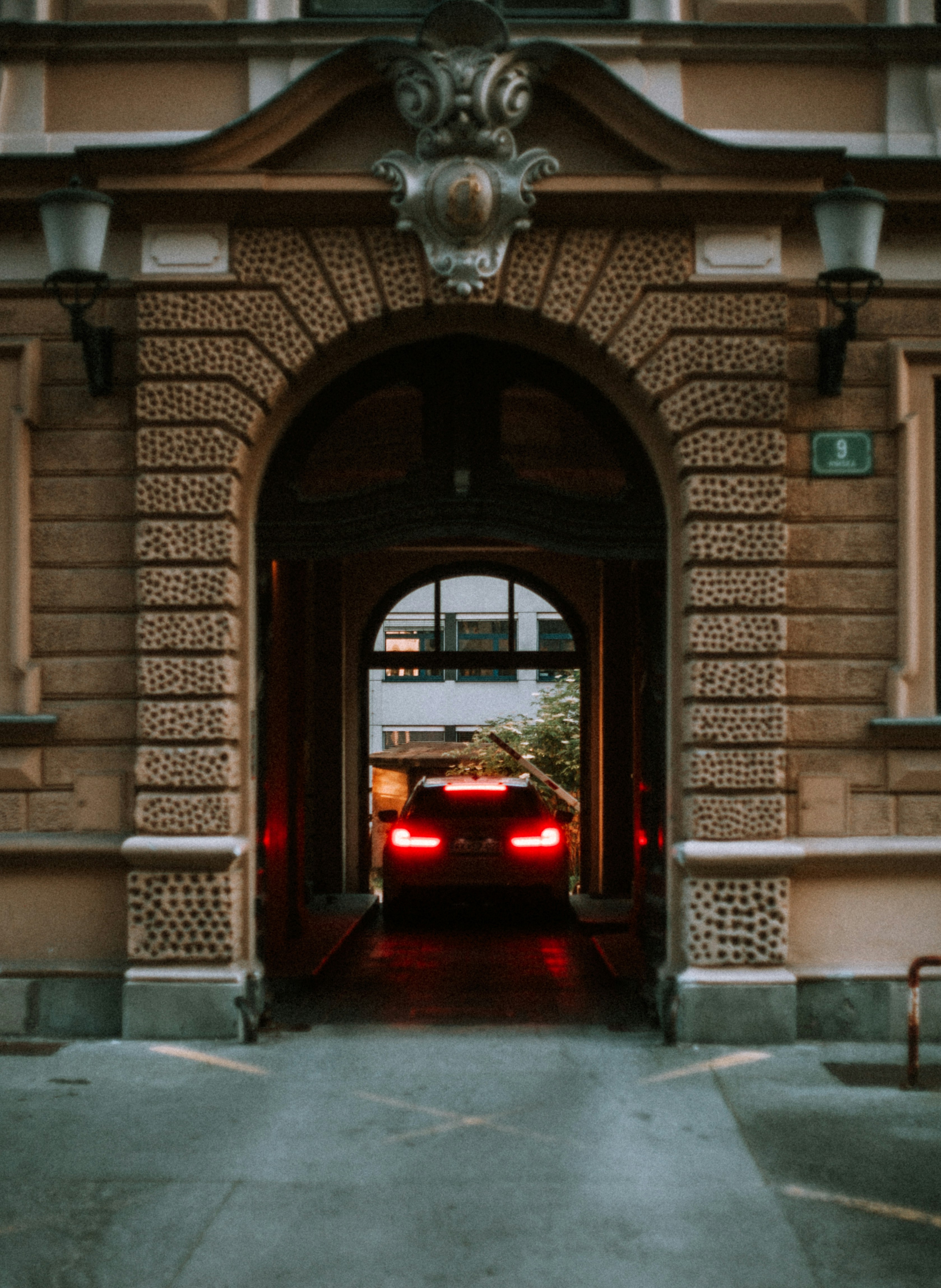 A sleek car emerges from an ornate archway, framed by textured stone walls and soft evening light.