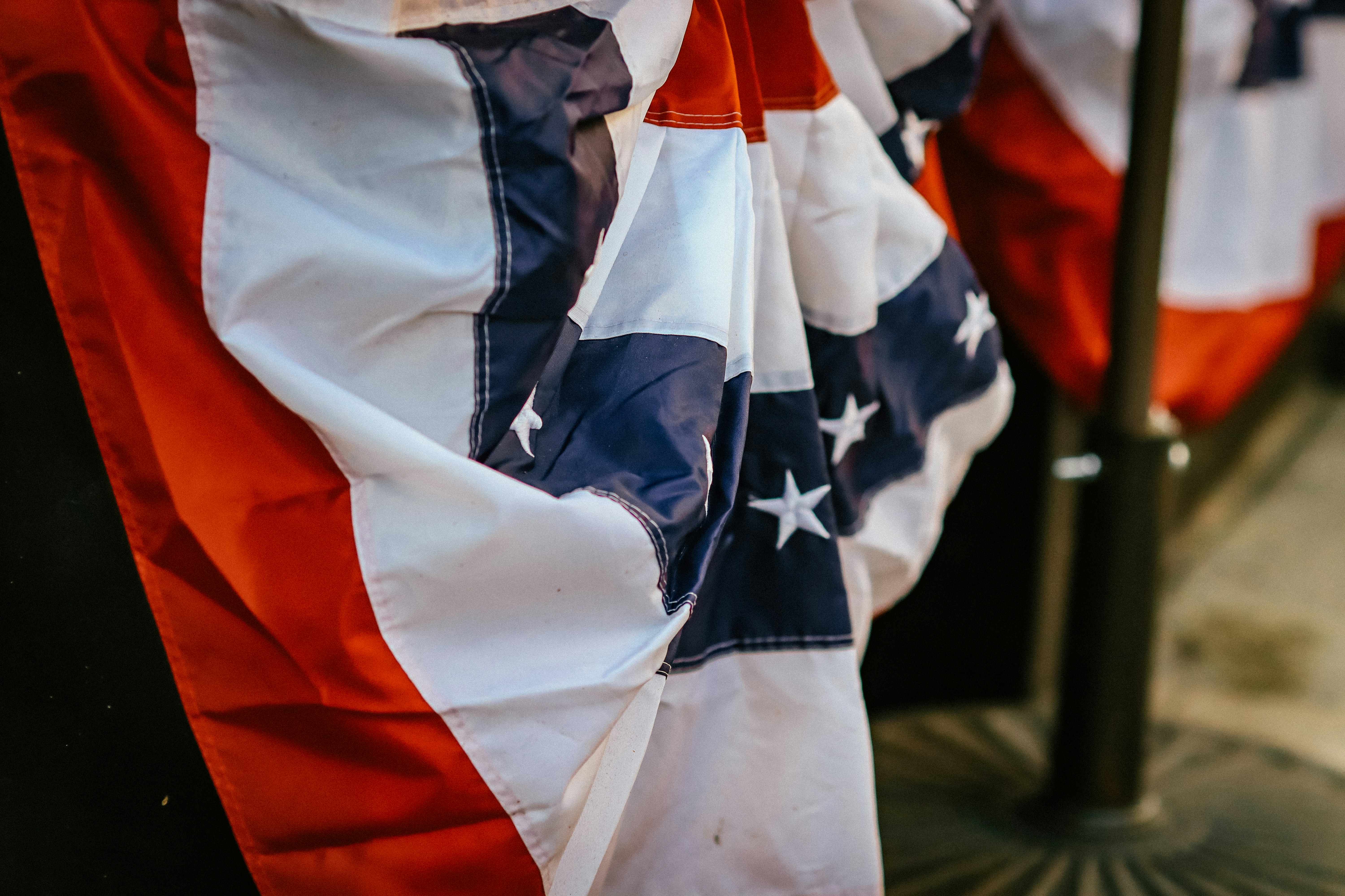 Close-up of an American flag draped elegantly, showcasing its vibrant colors and intricate design elements. The fabric folds create dynamic textures and shadows.
