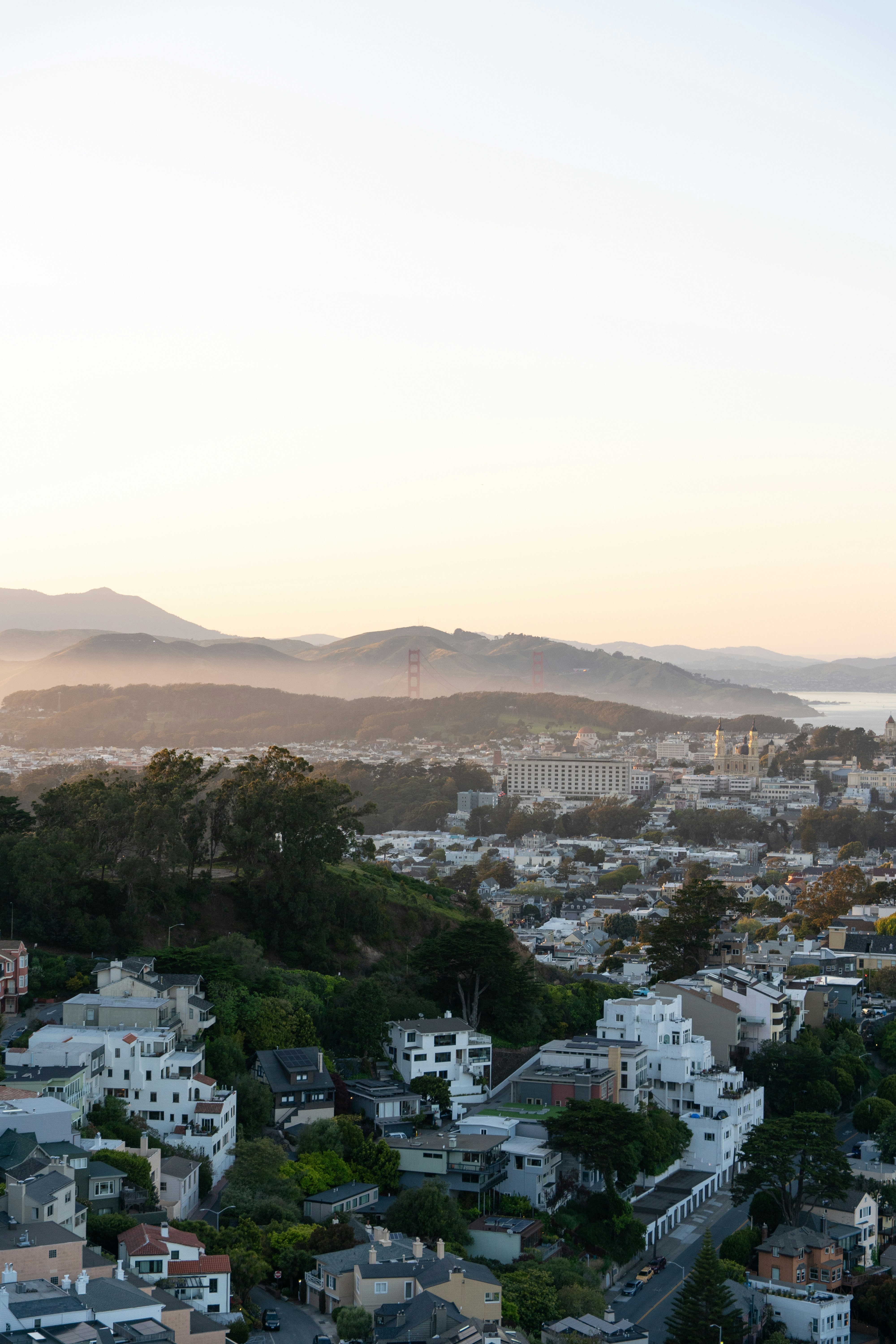 A panoramic view of San Francisco's landscape at dusk, showcasing the Golden Gate Bridge in the distance, surrounded by rolling hills and urban architecture.