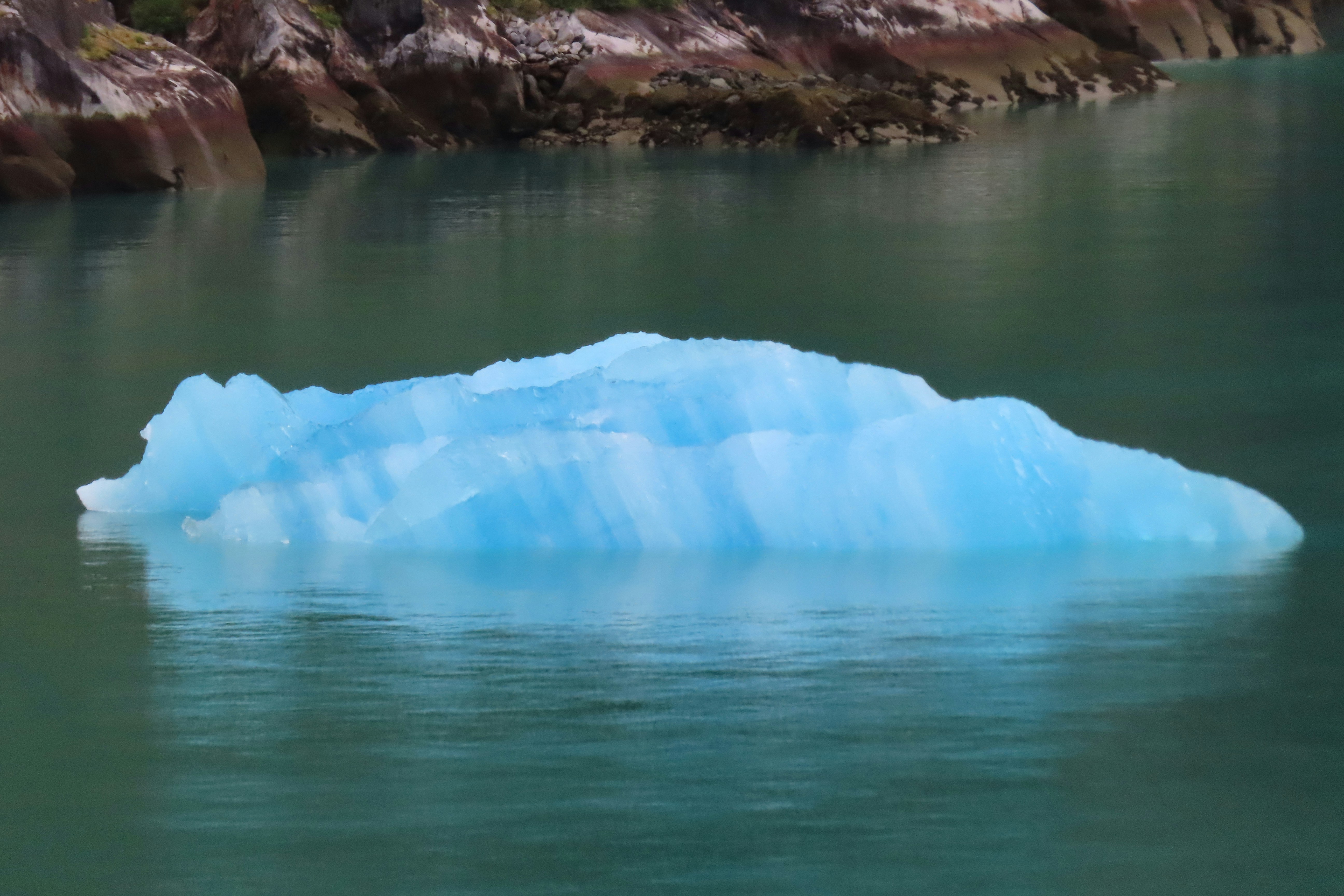 A bright blue iceberg floats on the water.