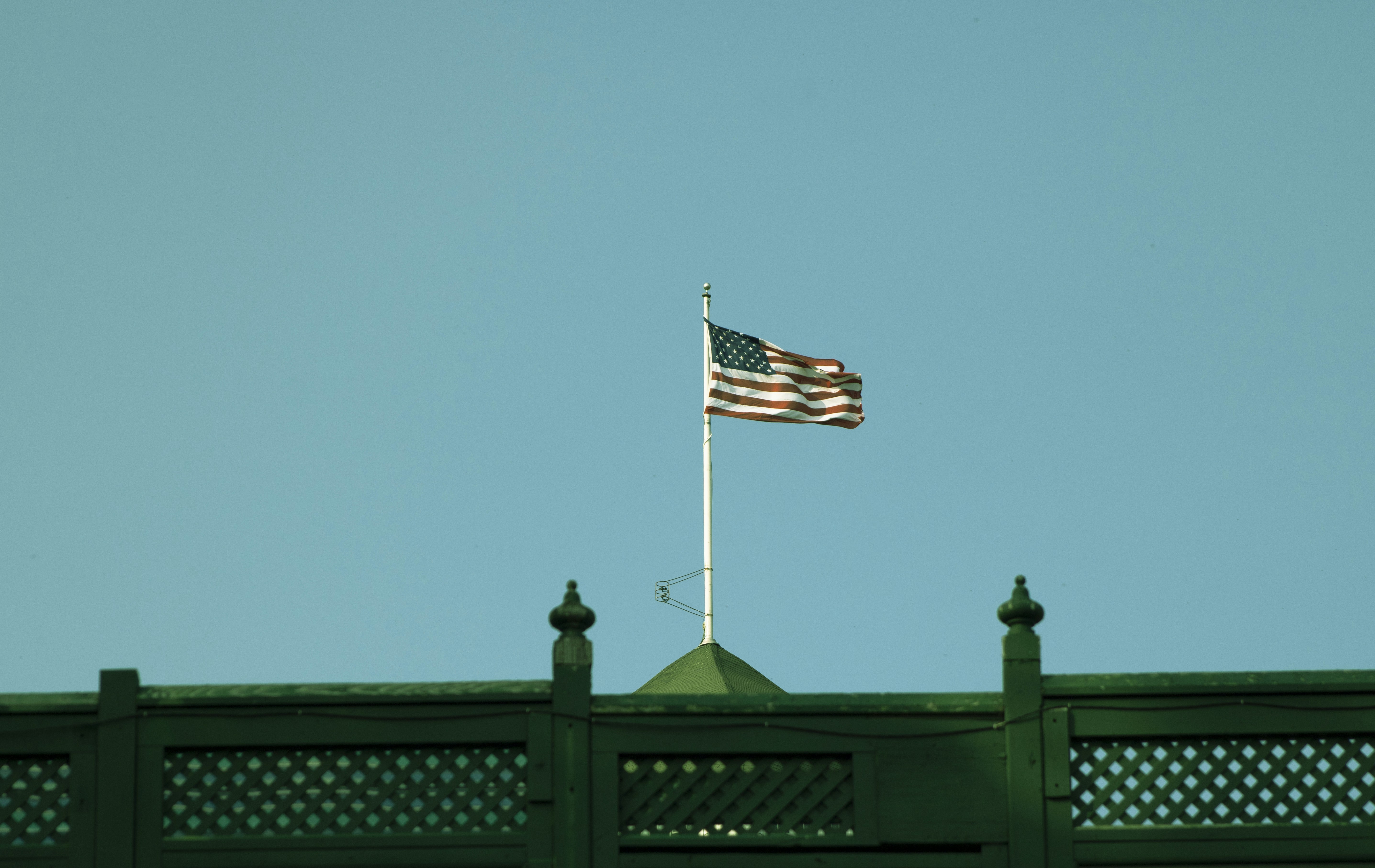 American flag waving atop a green structure against a clear blue sky.
