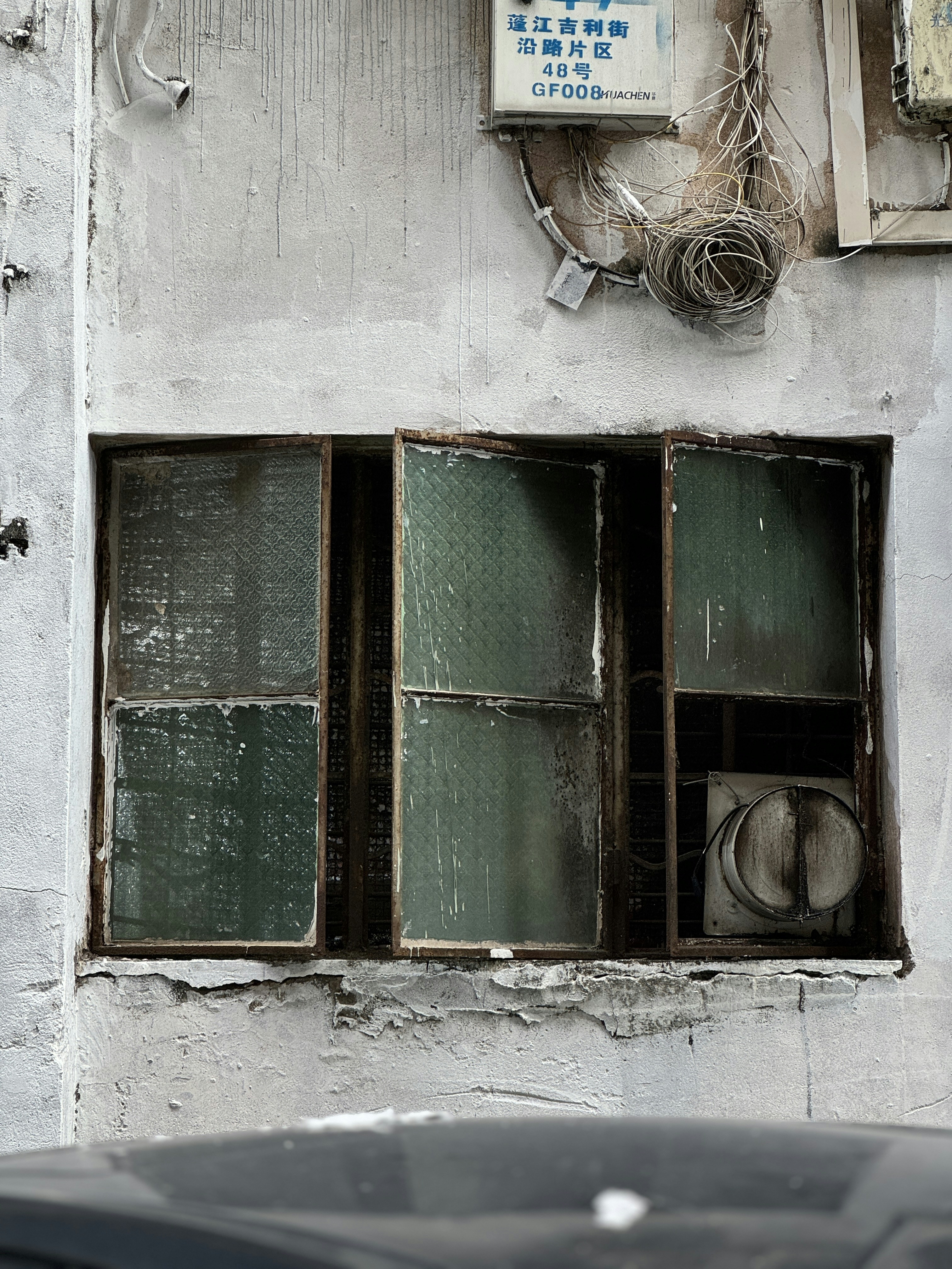 Weathered window with cracked glass and rusting frame, revealing glimpses of an abandoned interior. Urban setting reflects a sense of history and neglect.