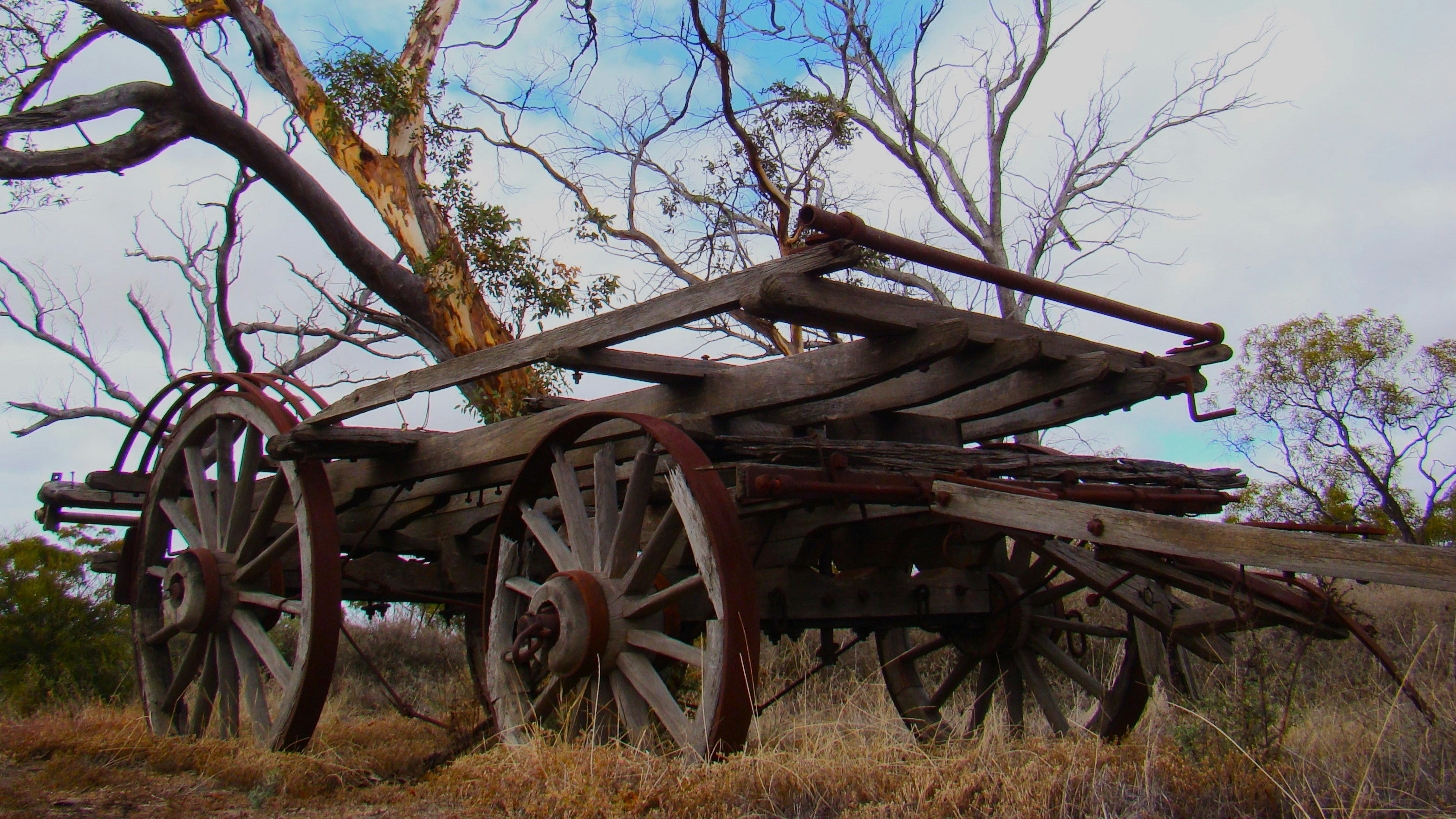 An old horsedrawn cart | An old, wooden wagon rests outdoors.