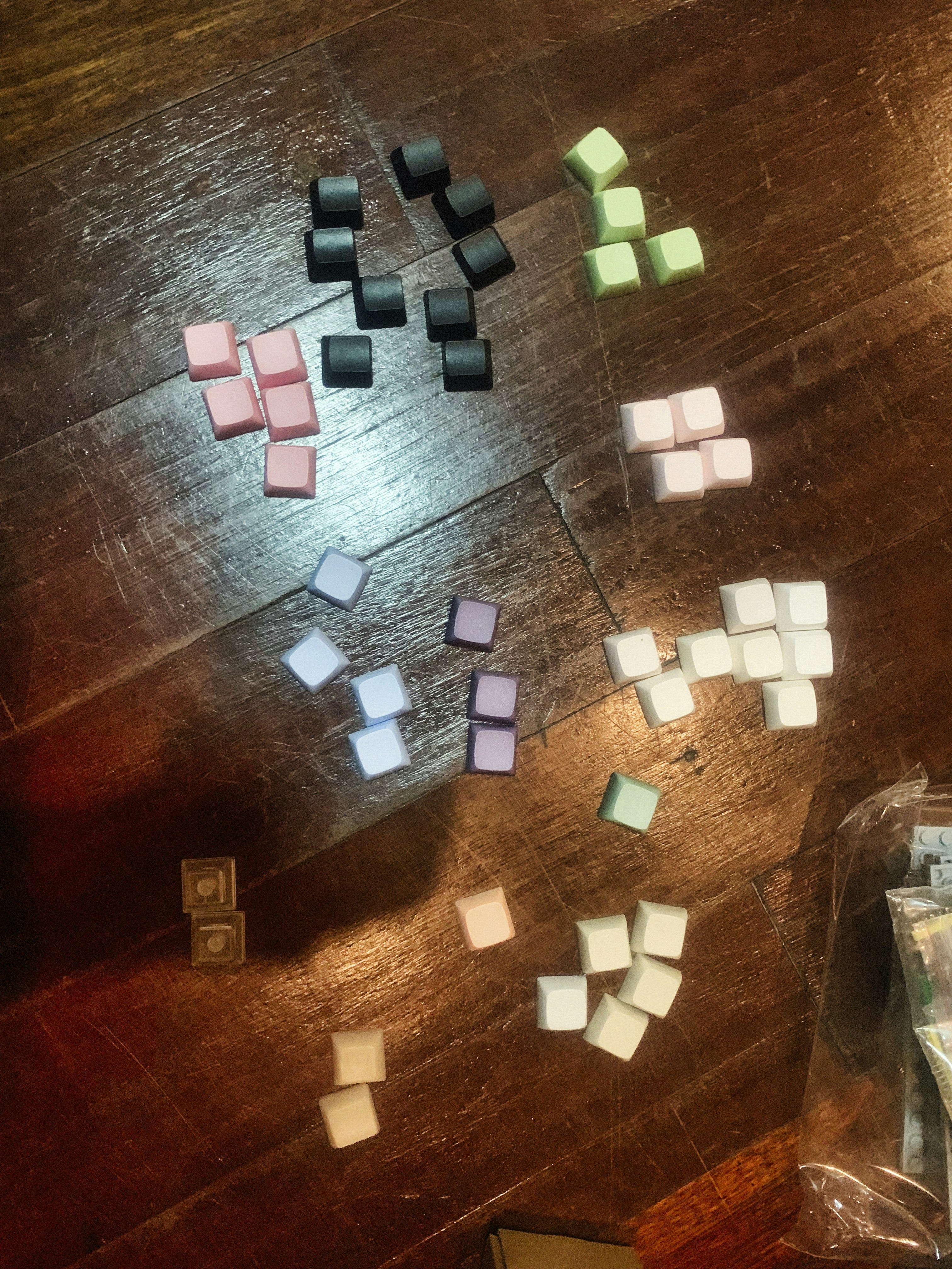 A vibrant assortment of small colored cubes scattered on a wooden surface, showcasing various shades including pink, black, green, and white.