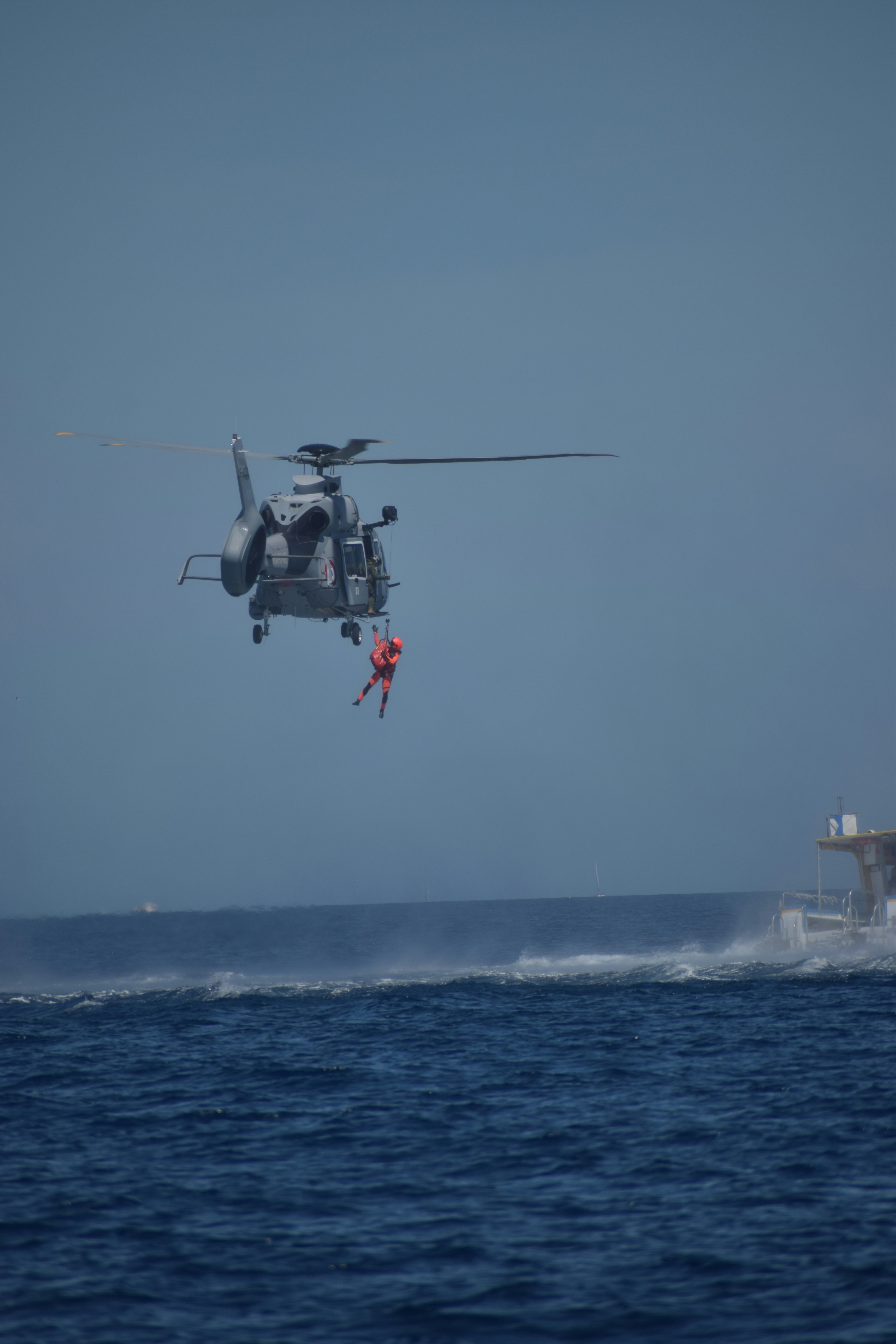 Helicopter performs a rescue operation over the ocean, with a rescuer suspended mid-air. The scene captures the intensity of emergency response efforts.