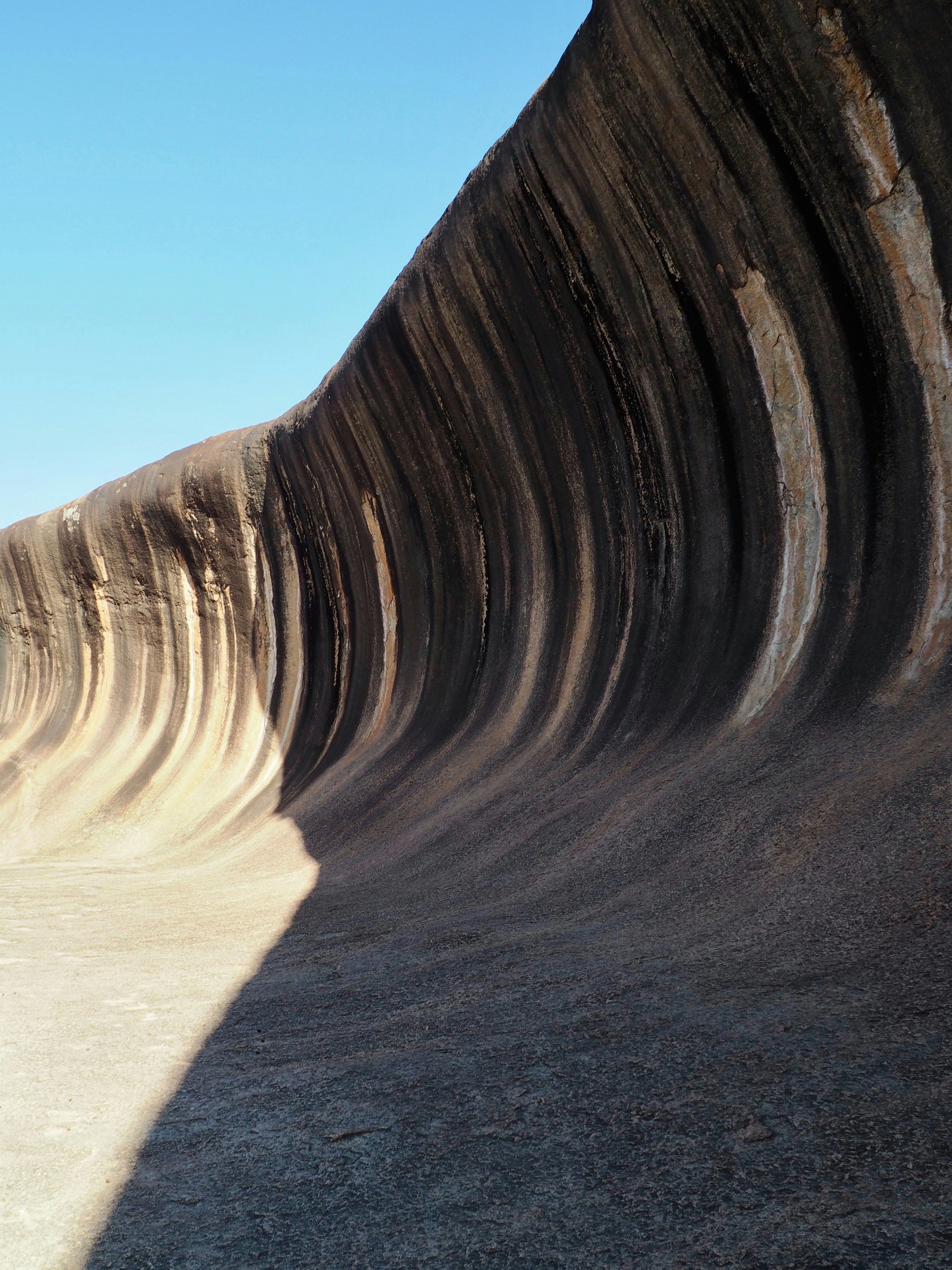 Curved sedimentary walls rise from a dusty ground under a clear blue sky, with dramatic shadows highlighting the circular striations; a canyon-like tunnel forms a natural sculpture.