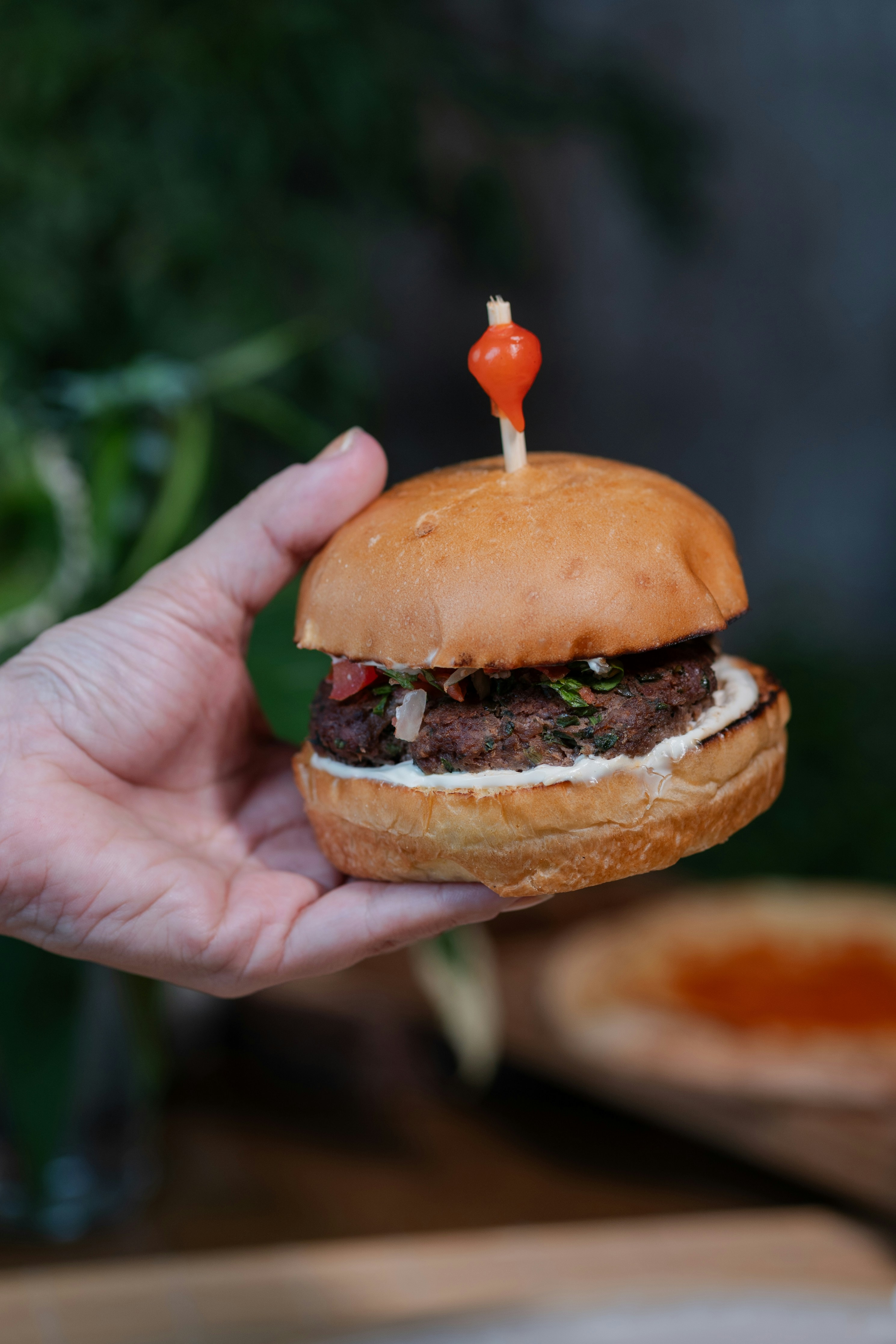 Cherry-Topped Skewer Holds a Juicy Handheld Burger in a Sunlit Garden