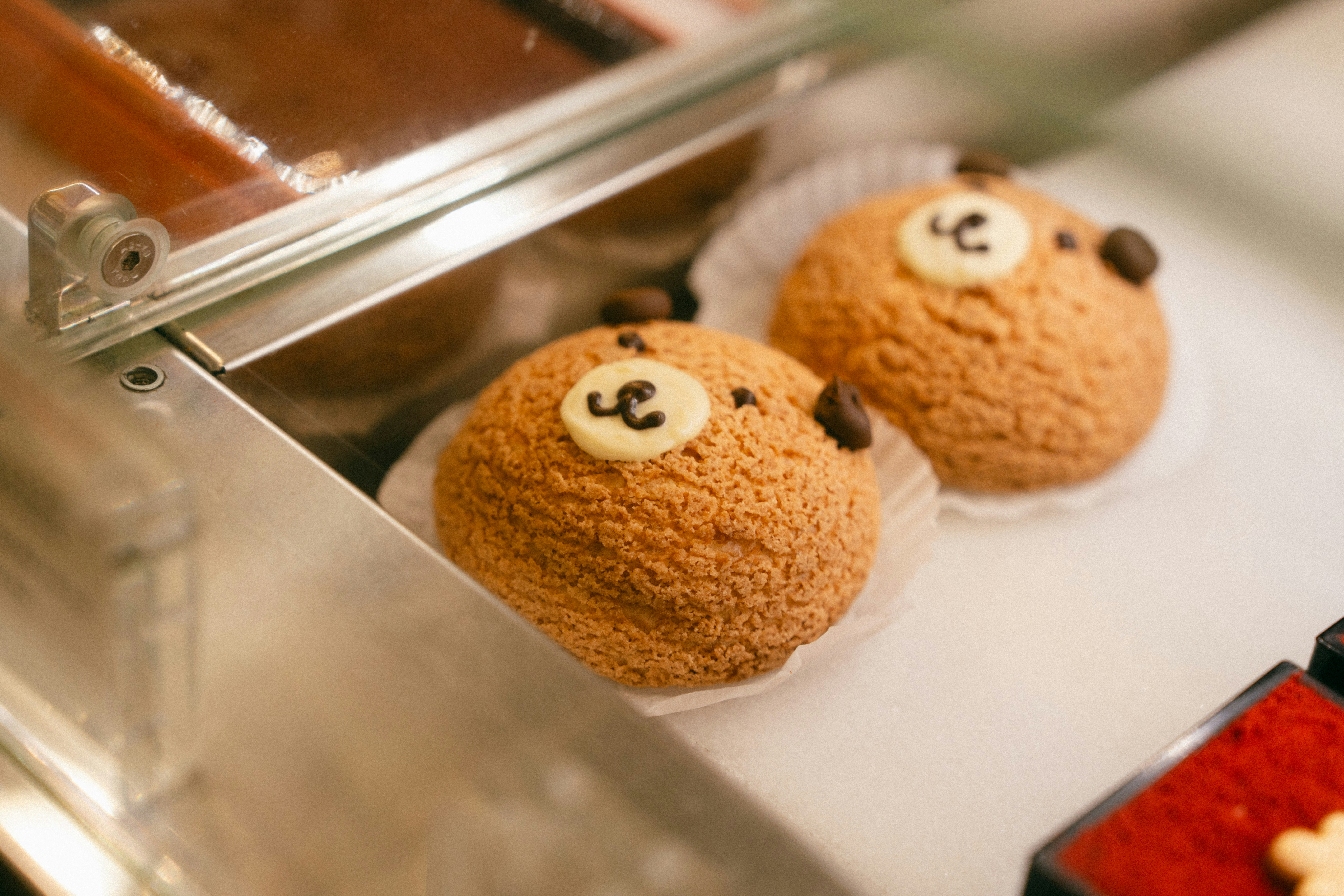 Two adorable bear-shaped pastries displayed in a bakery case, showcasing their charming faces and textured surfaces.