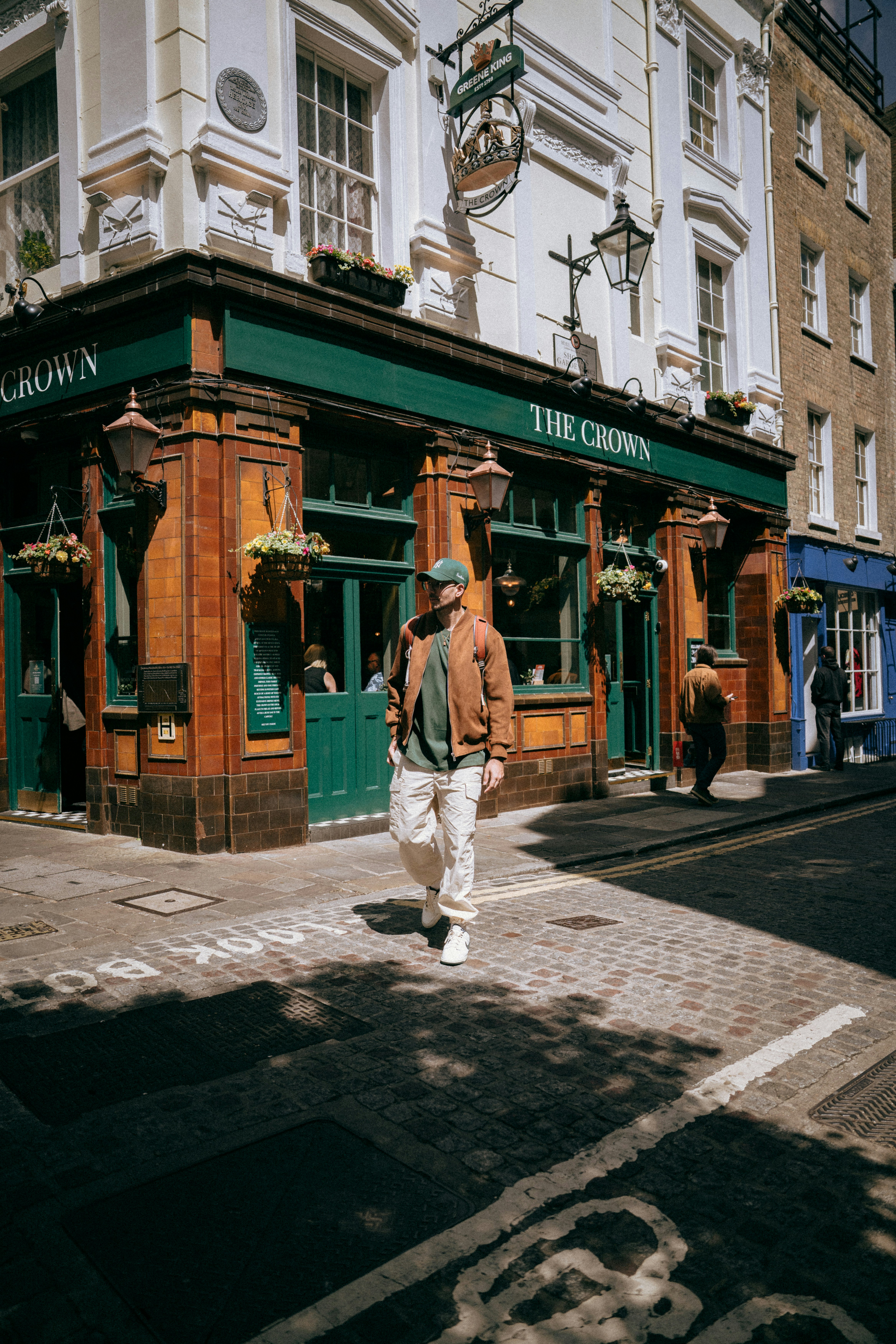 A casually dressed man walks past The Crown pub, showcasing a vibrant street scene with charming architecture and lively storefronts.