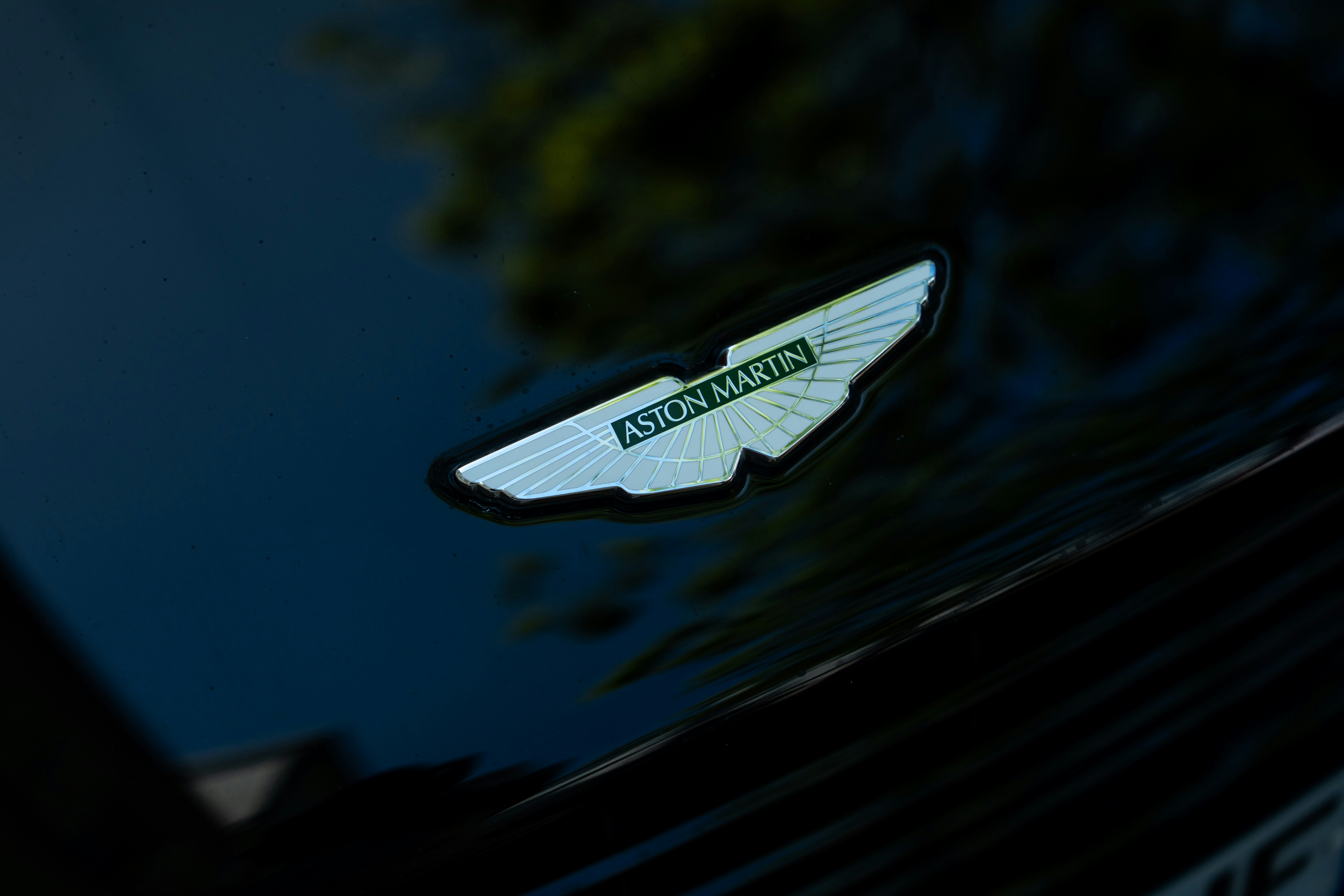 Midnight Crest on a Lacquered Hood: Aston Martin badge in a gleaming reflection