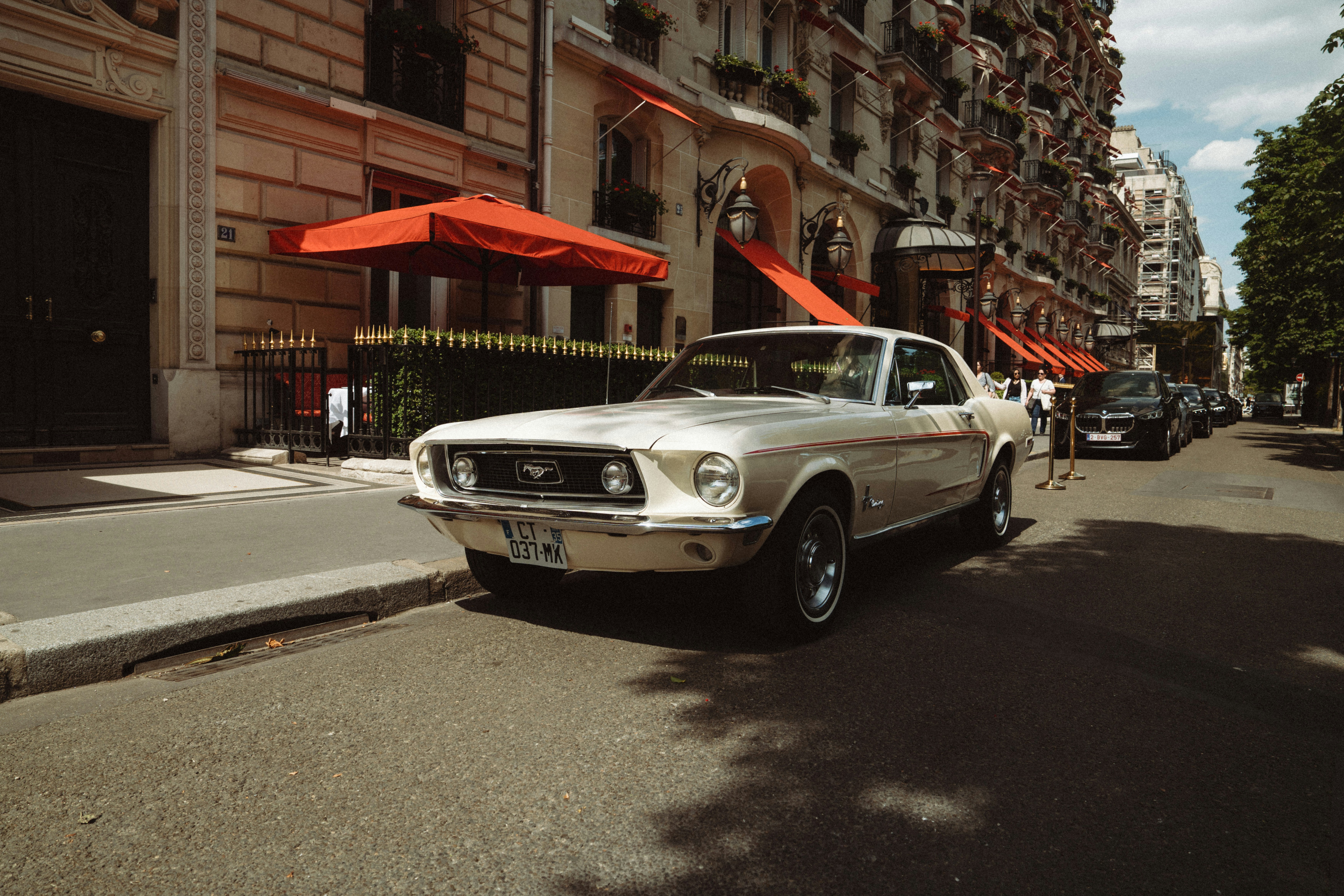 Sunlit Streetcar: A White 1960s Mustang on a Red-umbrella Lane