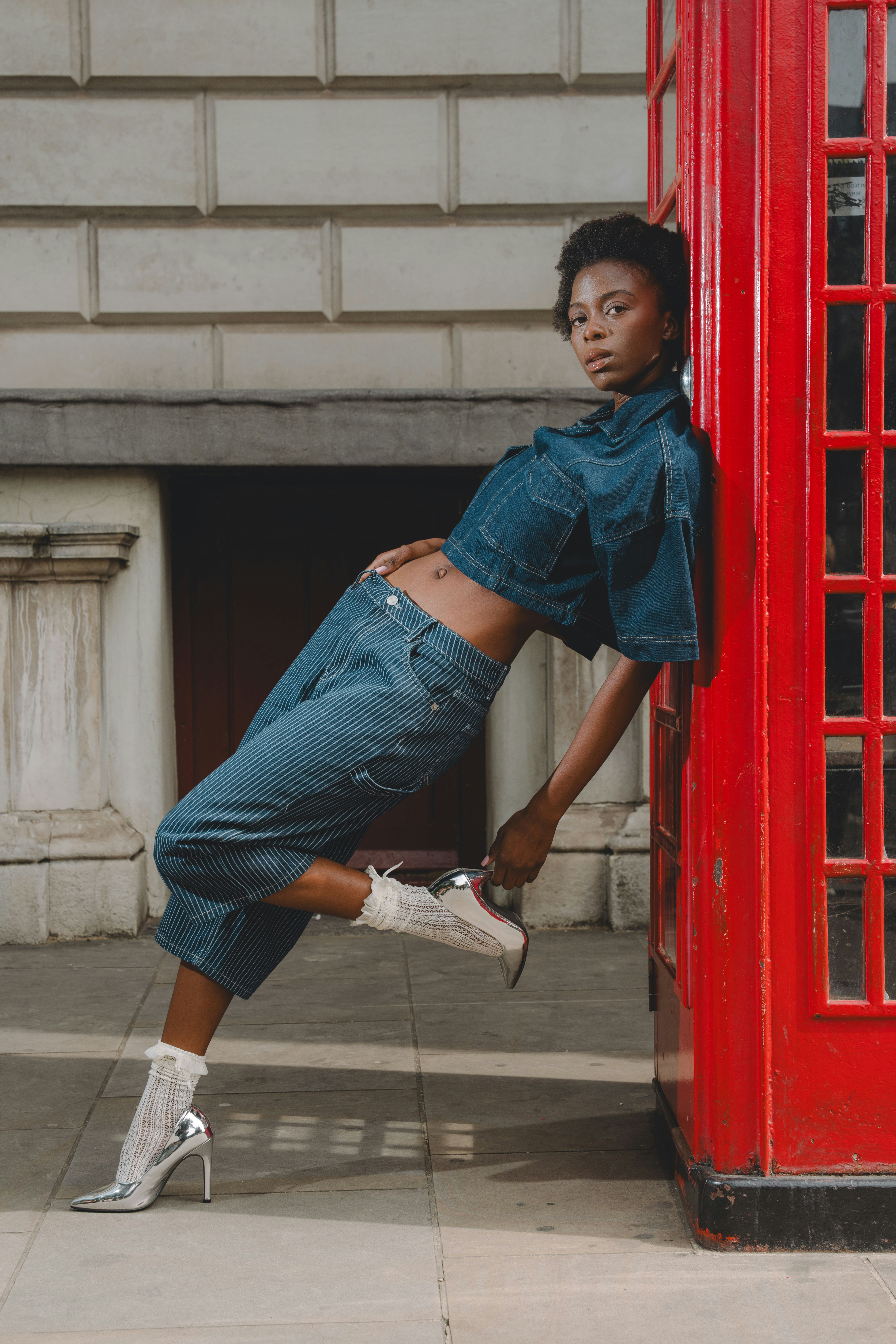 Woman poses next to a red phone booth. photo – Free Fashion Image on ...