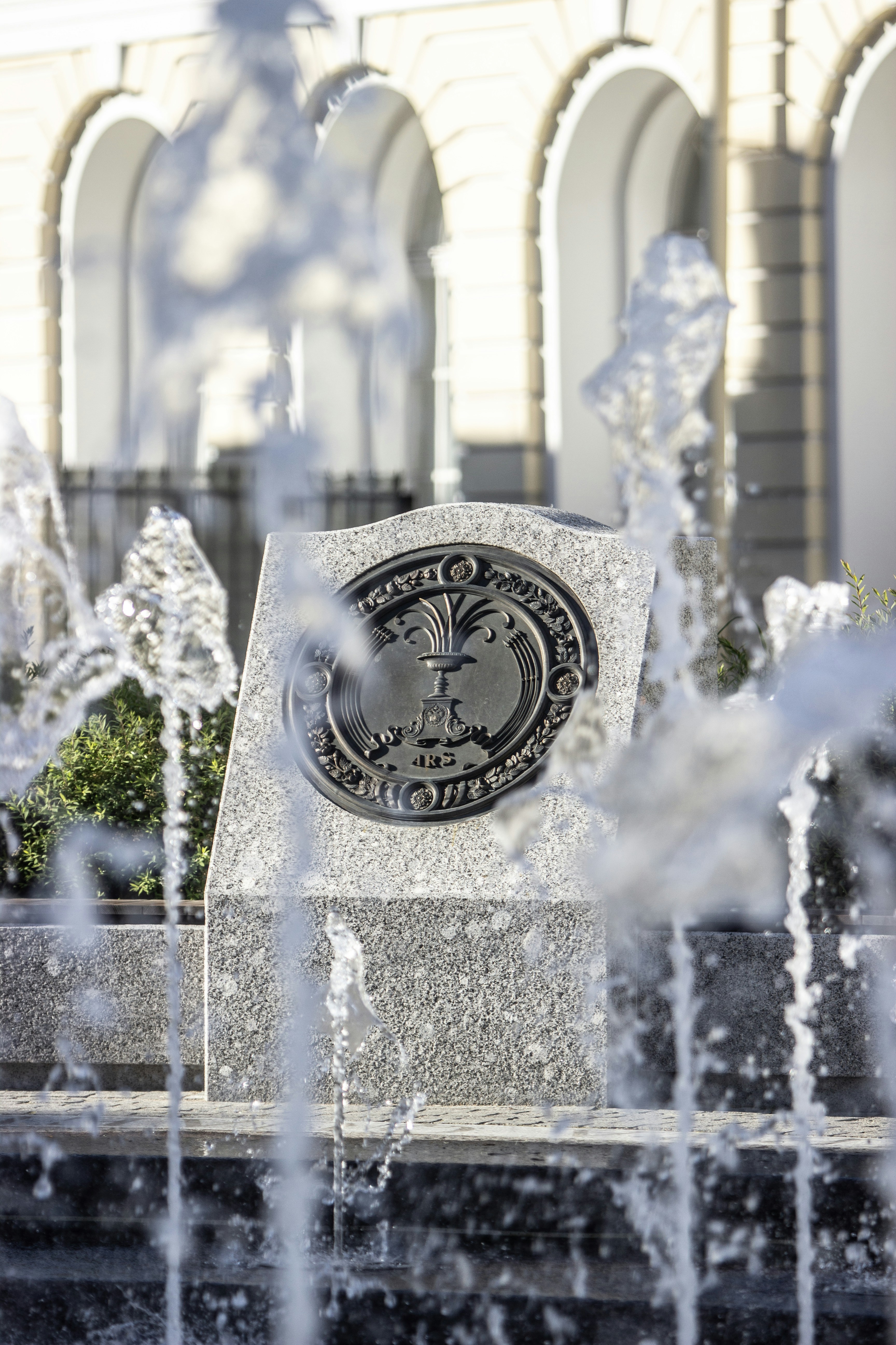 Stone emblem in a sunlit fountain framed by arched facade