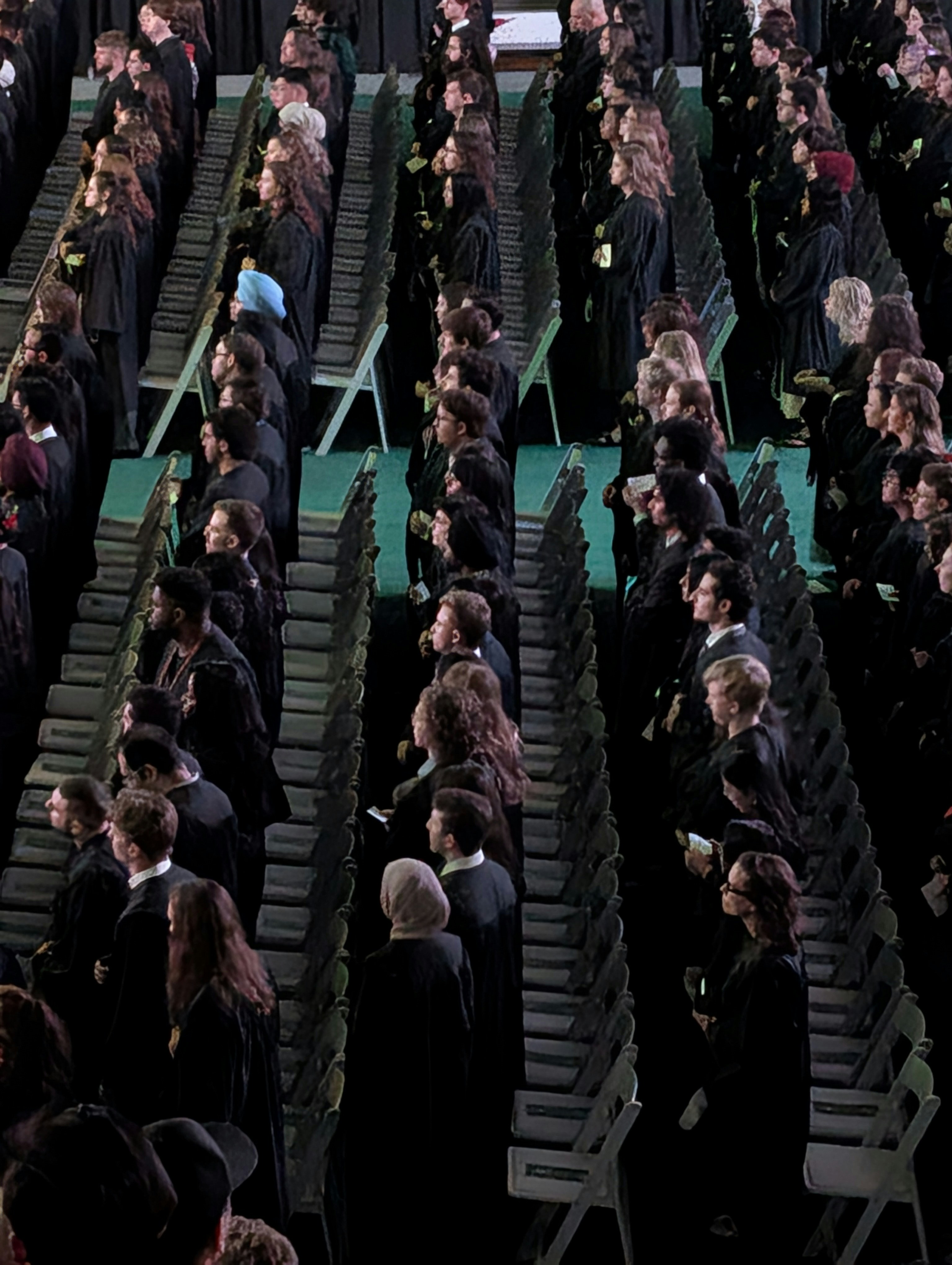 Graduates in black gowns and caps stand in unison during a commencement ceremony, showcasing a moment of collective achievement.