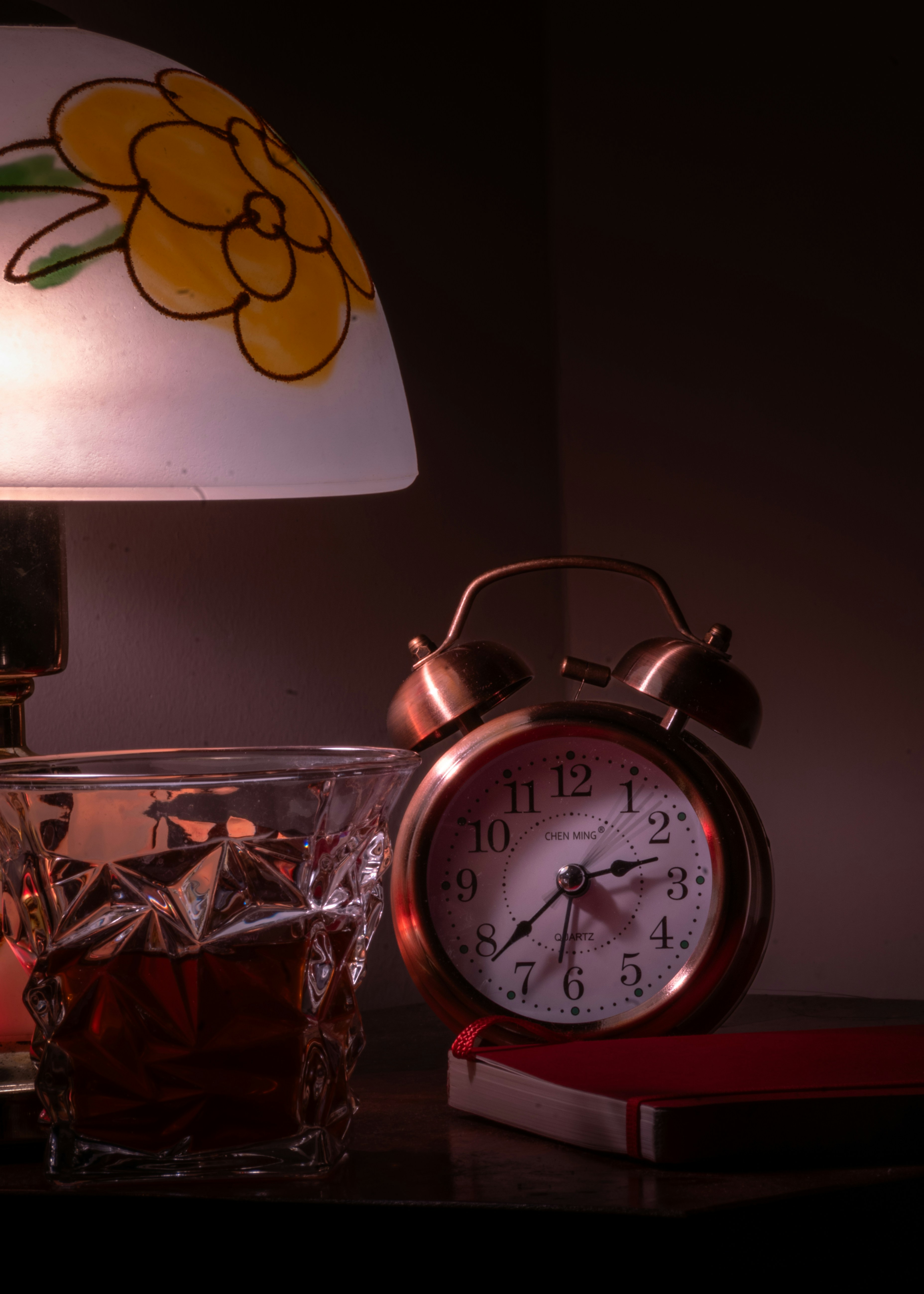 Copper Clock Vigil by Crystal Glass Under Warm Floral Light