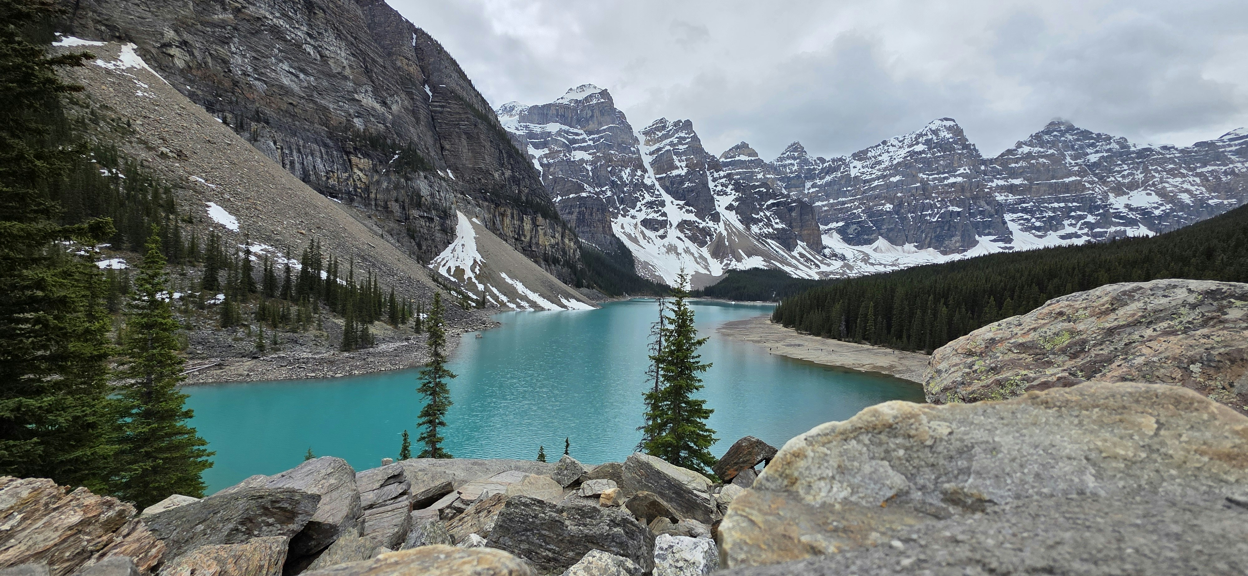 Turquoise waters of Moraine Lake framed by rugged mountains and evergreen trees, showcasing a serene natural landscape.